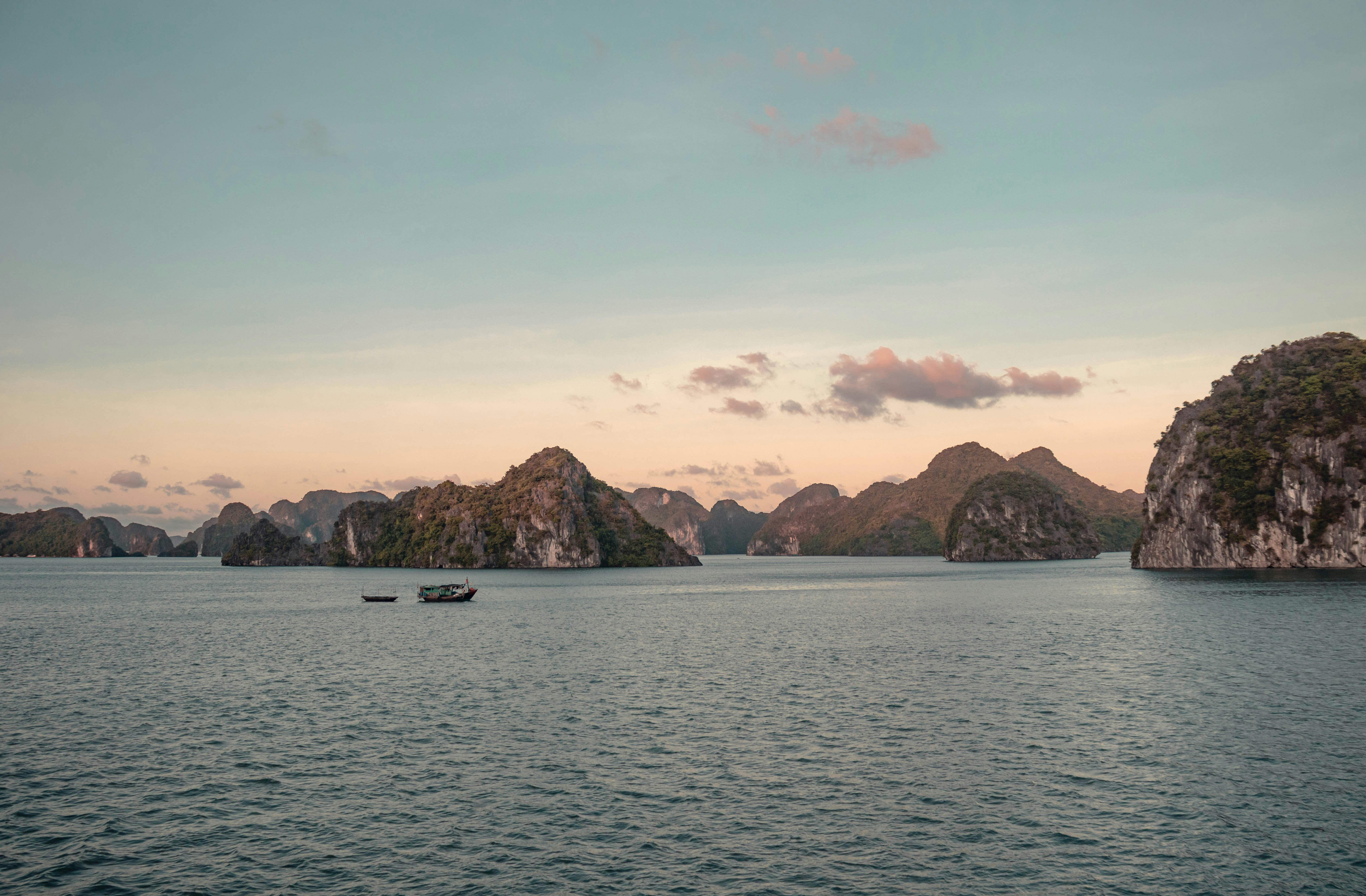 Serene bay with limestone islands under a pastel sky at sunset.