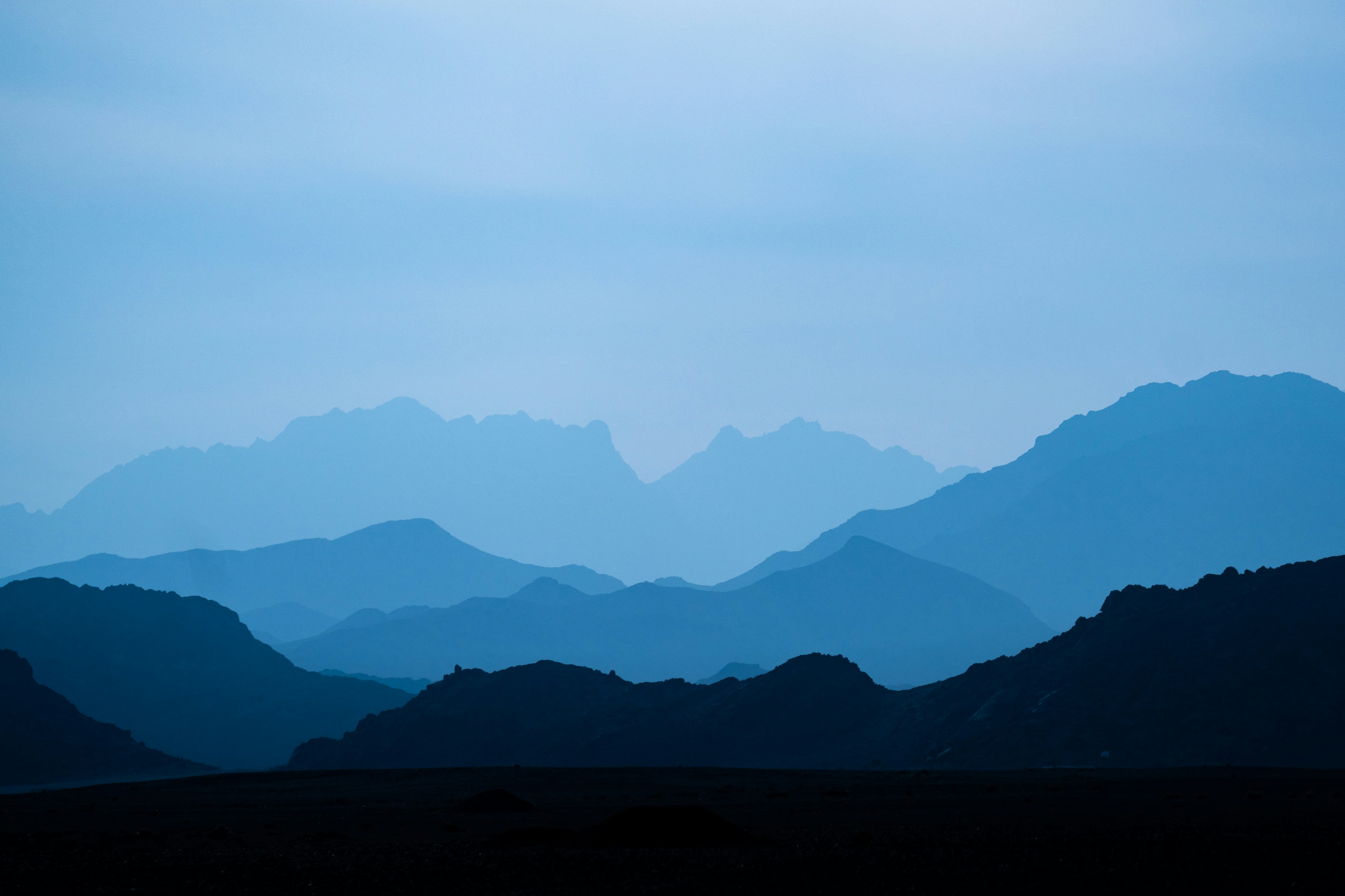 Layered mountain silhouettes under a soft blue sky at dusk.