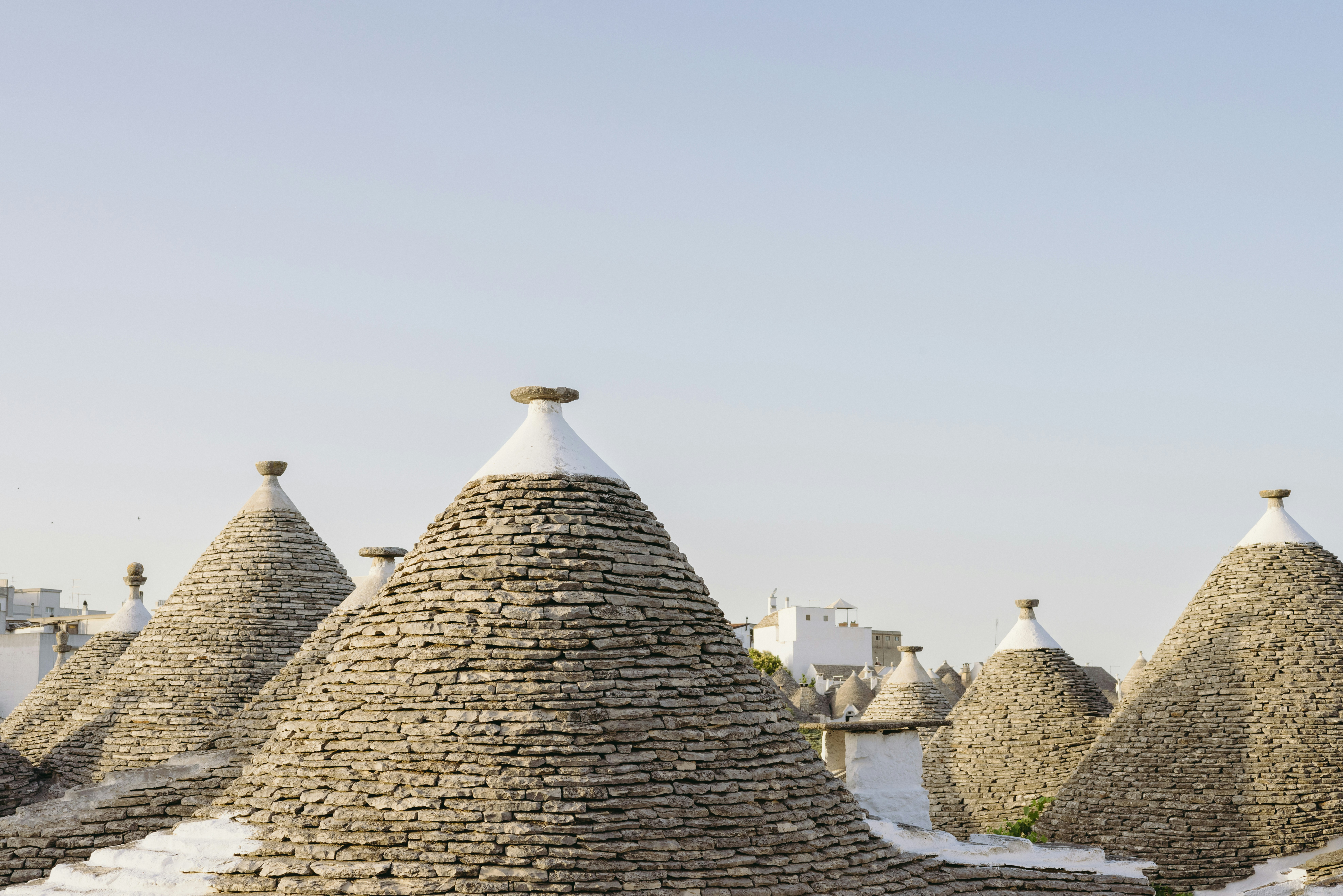 Traditional stone trulli houses with conical roofs against a clear blue sky.