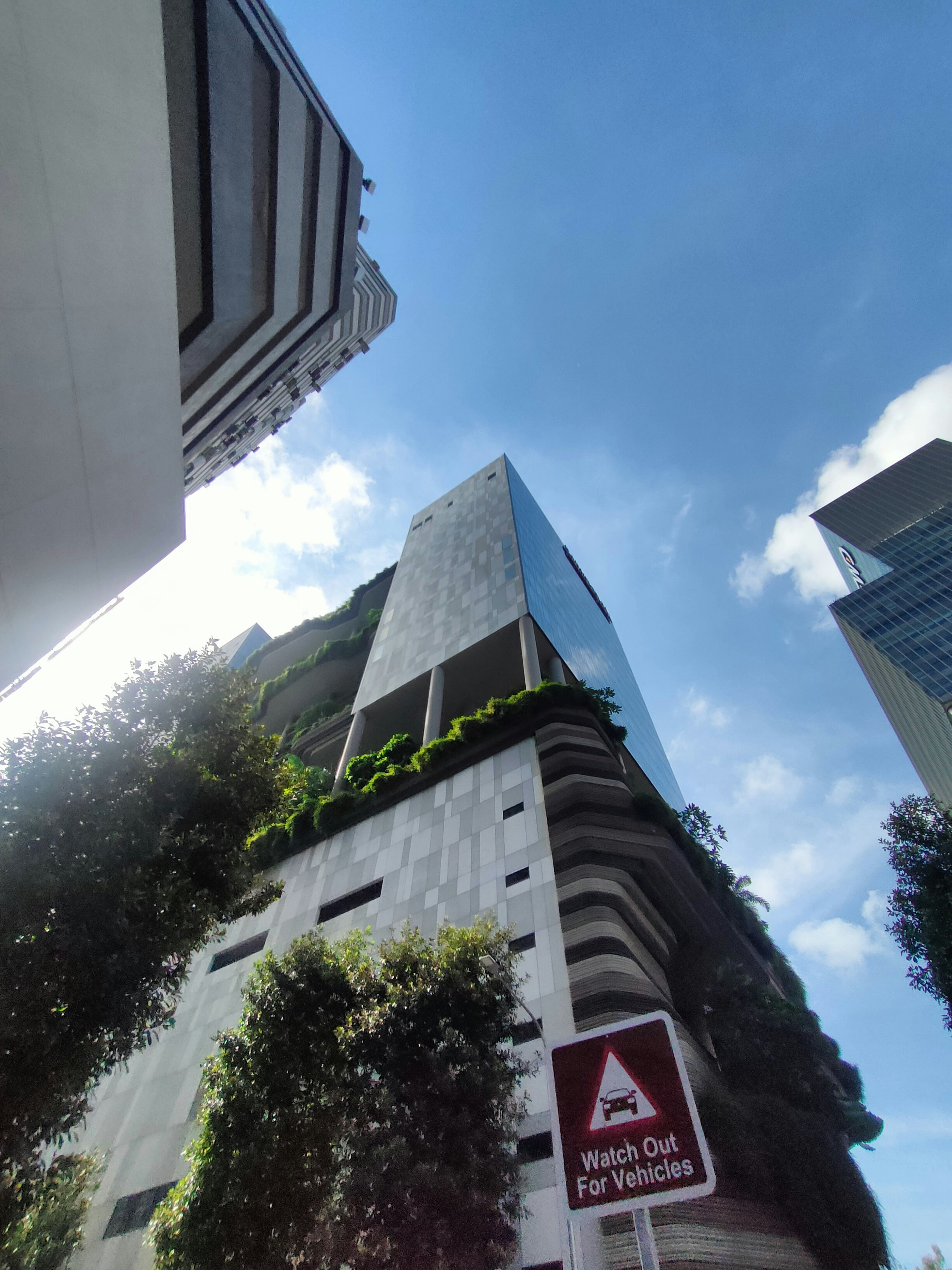 A striking modern building adorned with greenery, viewed from below against a vibrant blue sky. The composition highlights the integration of nature and urban design.