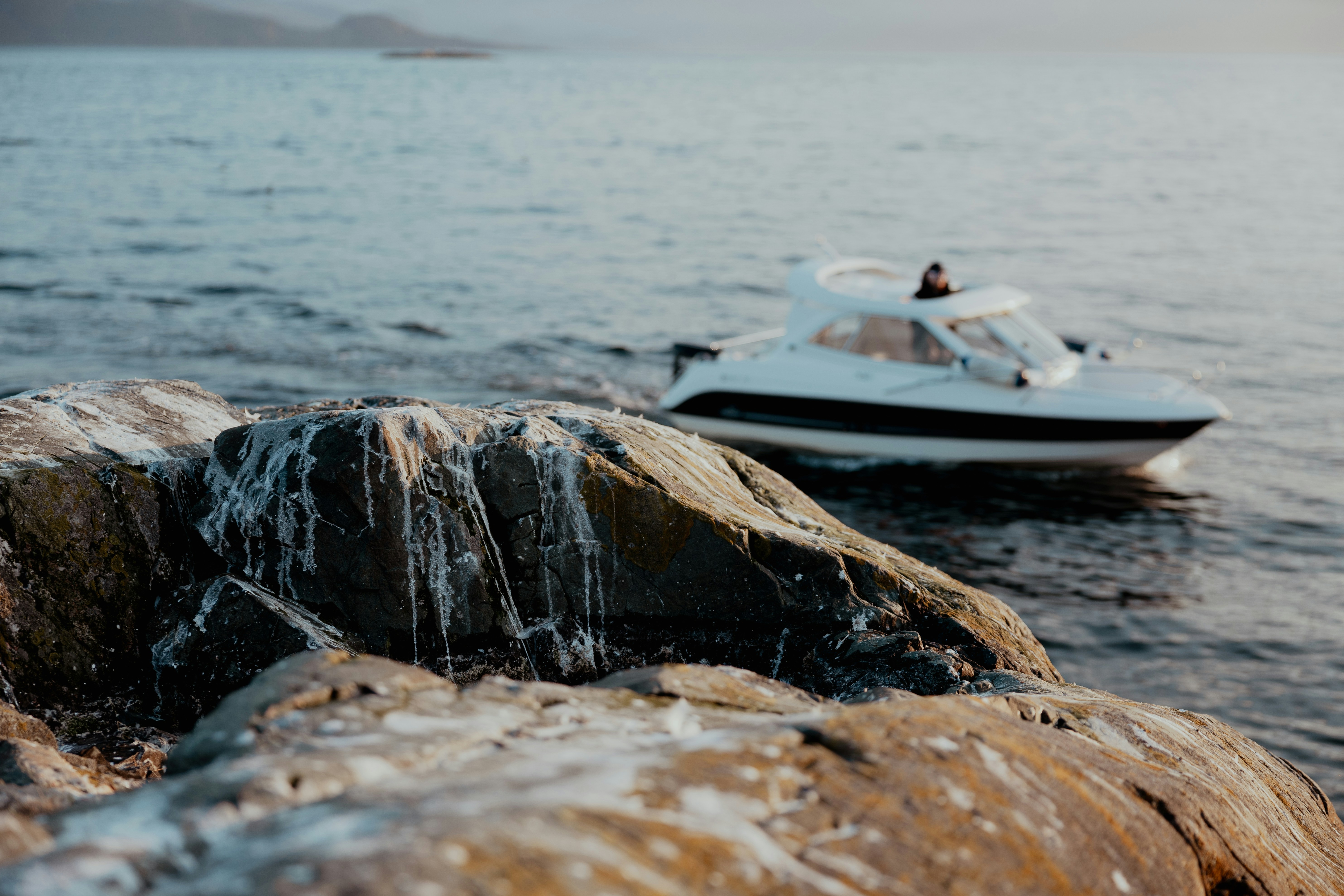 White motorboat gliding past rugged coastal rocks at sunset.