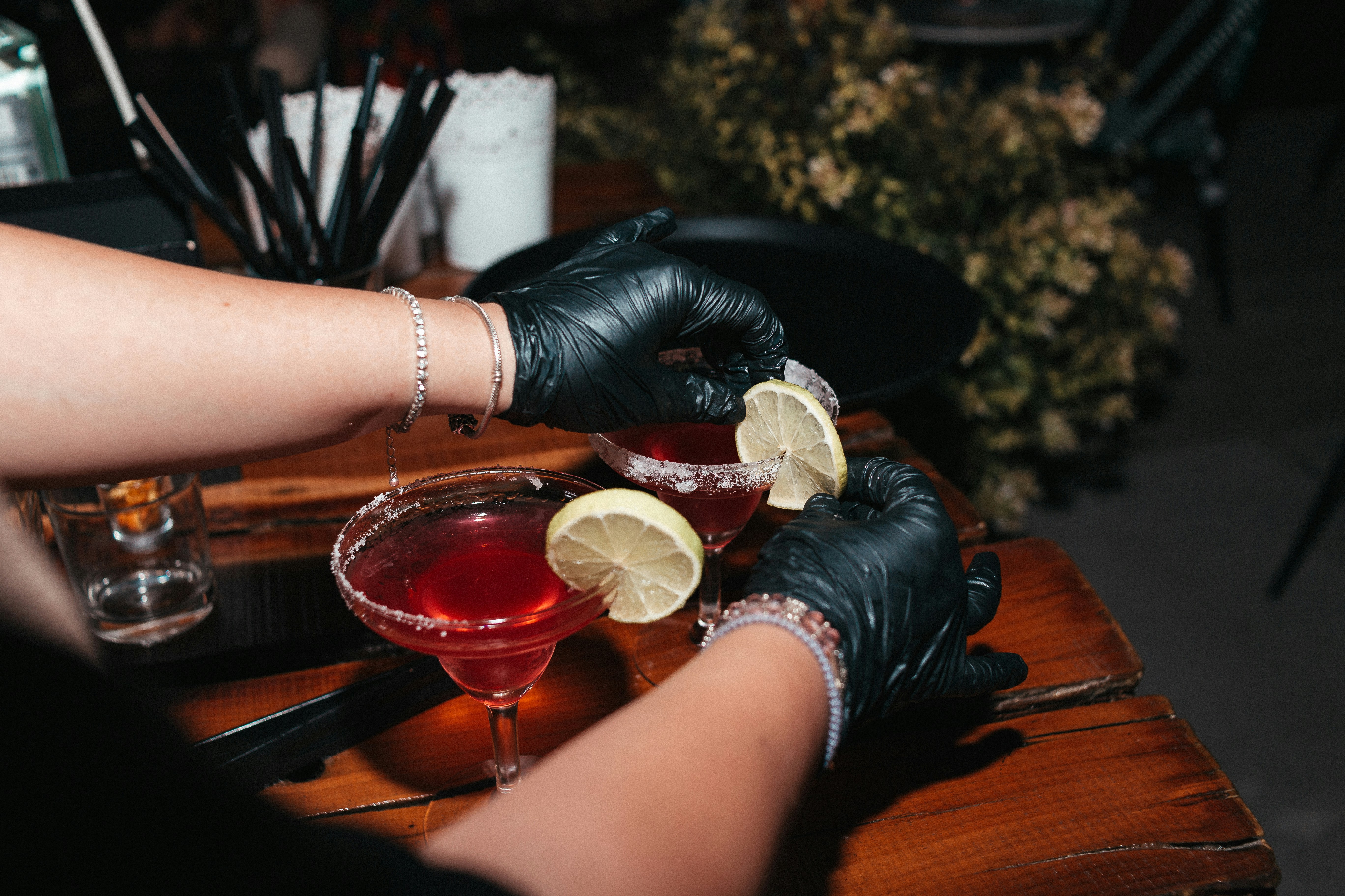 Scarlet Garnish: Gloved Hands Craft Crimson Cocktails at a Wooden Bar