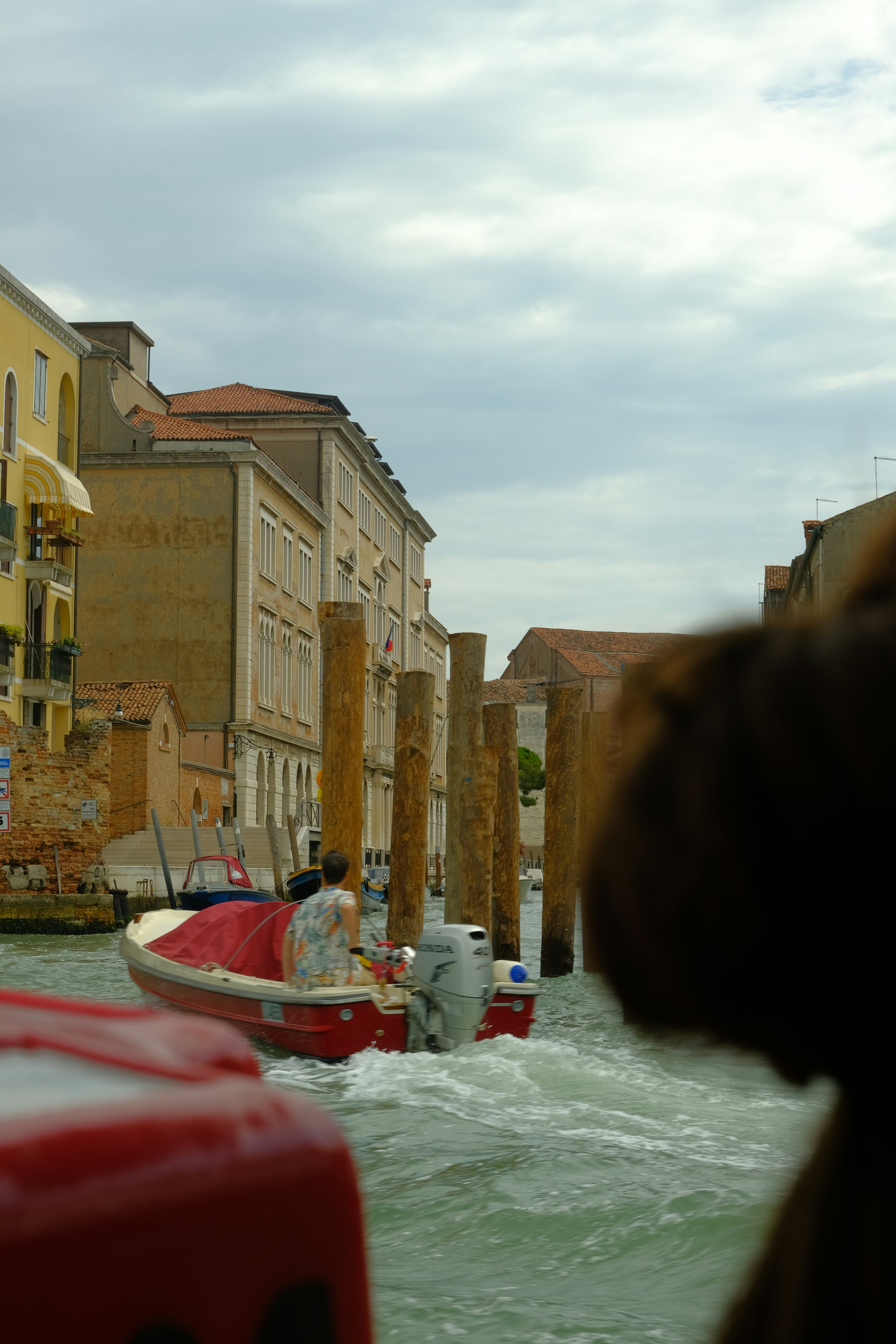 Red Motorboat Traverses a Venetian Canal, Framed by Weathered Columns