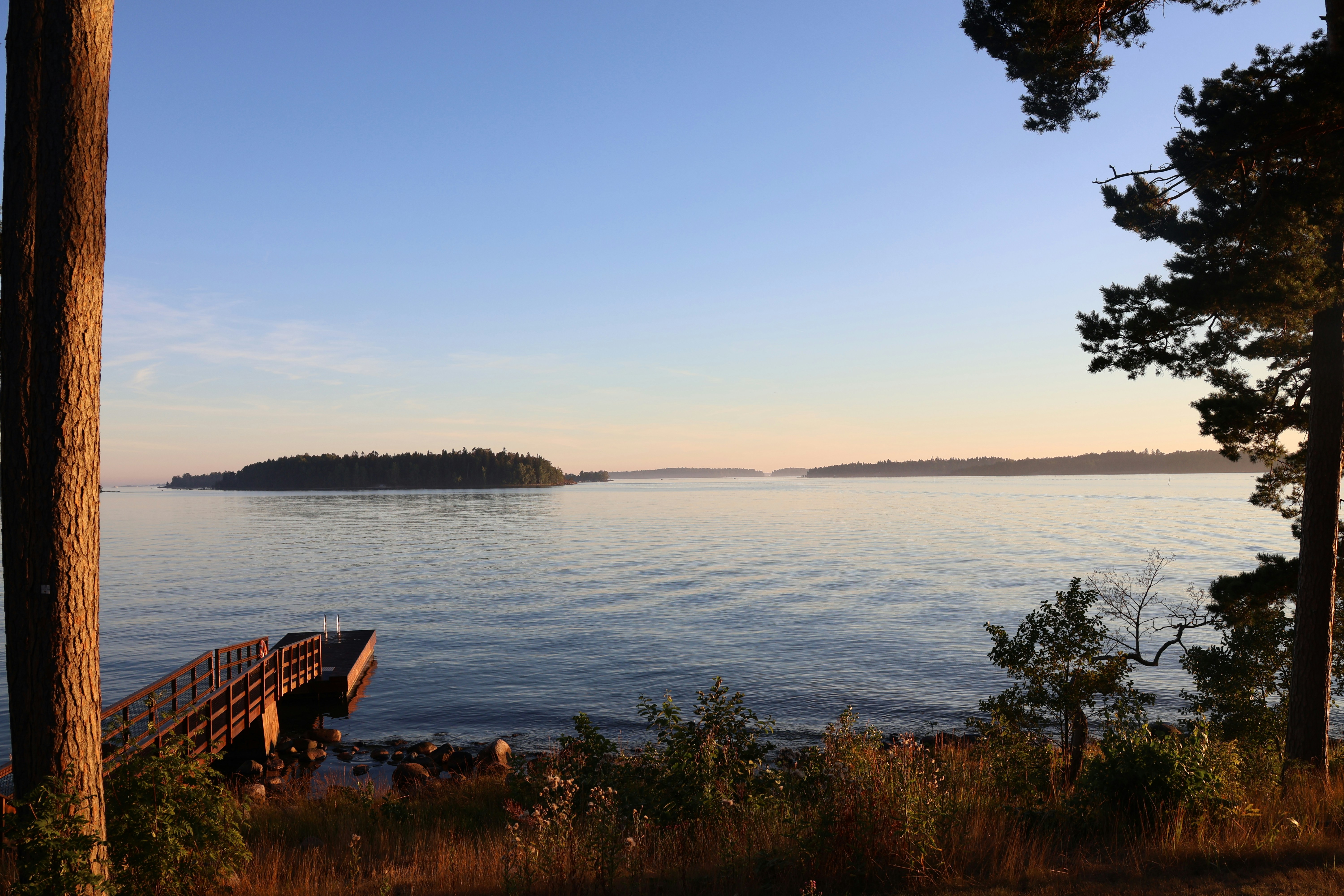 Serene coastal scene with a wooden dock overlooking calm waters and distant islands at sunset.