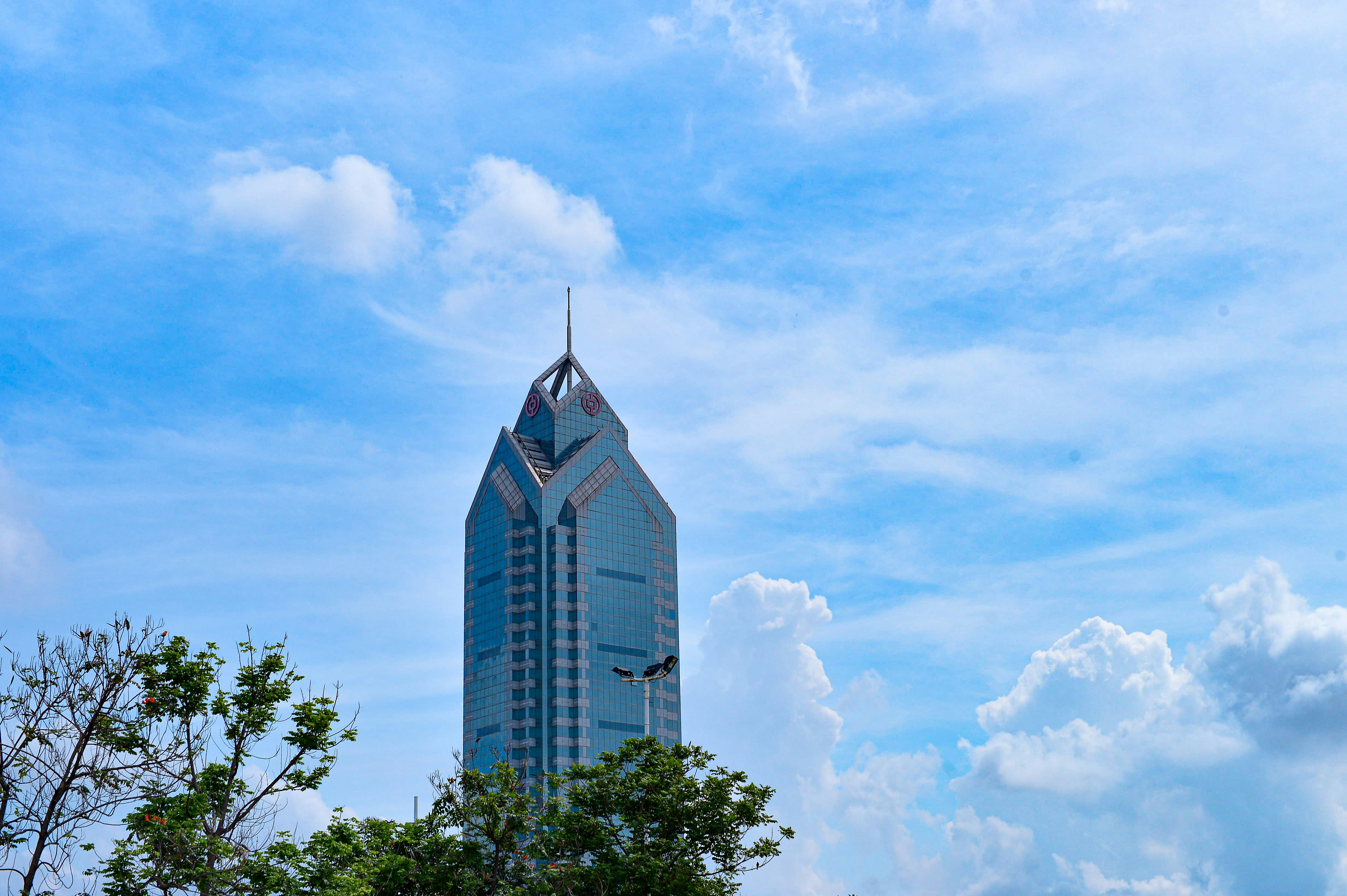 Blue Glass Spire Rising Above a Green Canopy Under a Clear Sky