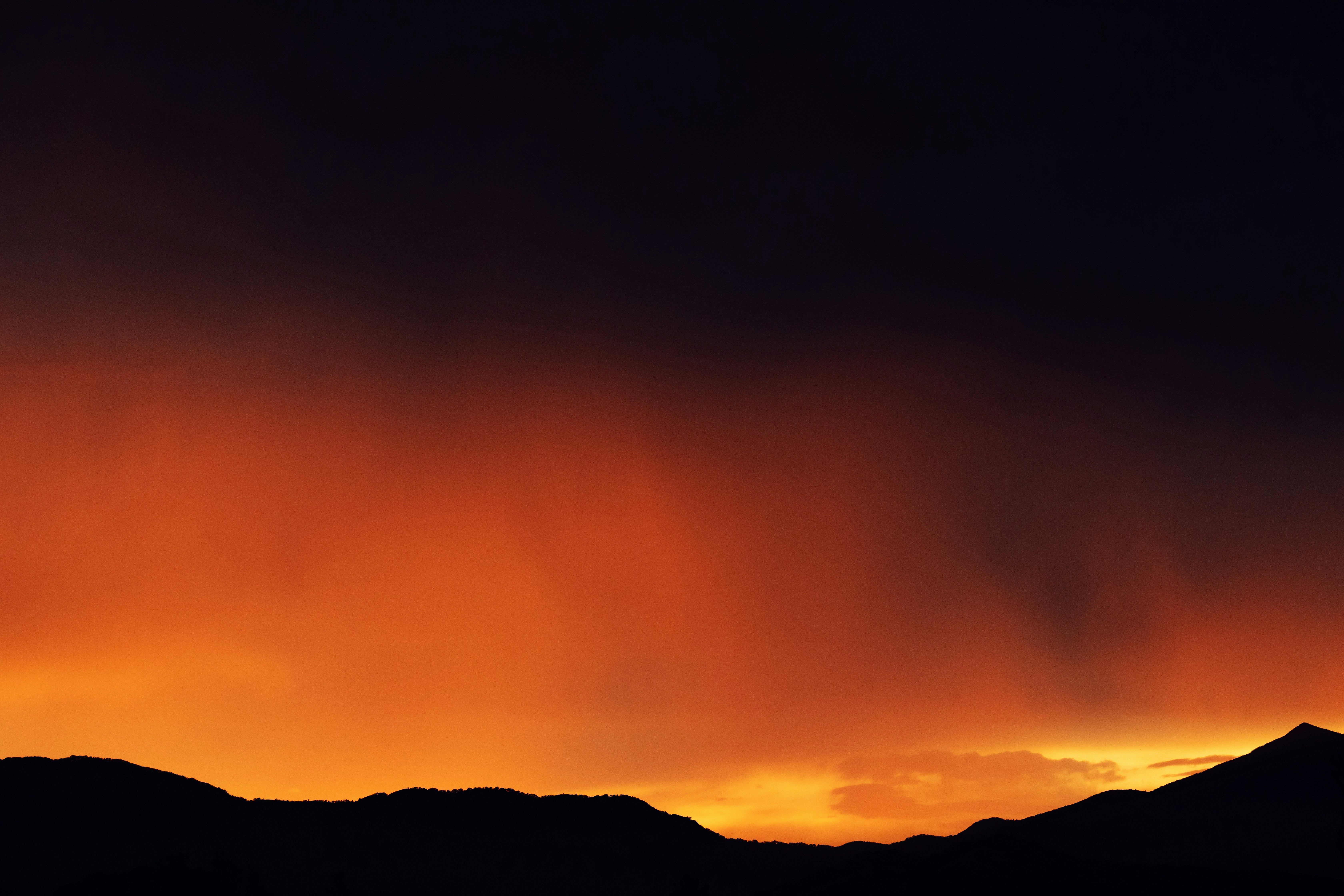 Vibrant orange hues illuminate the sky above silhouetted mountains at dusk.