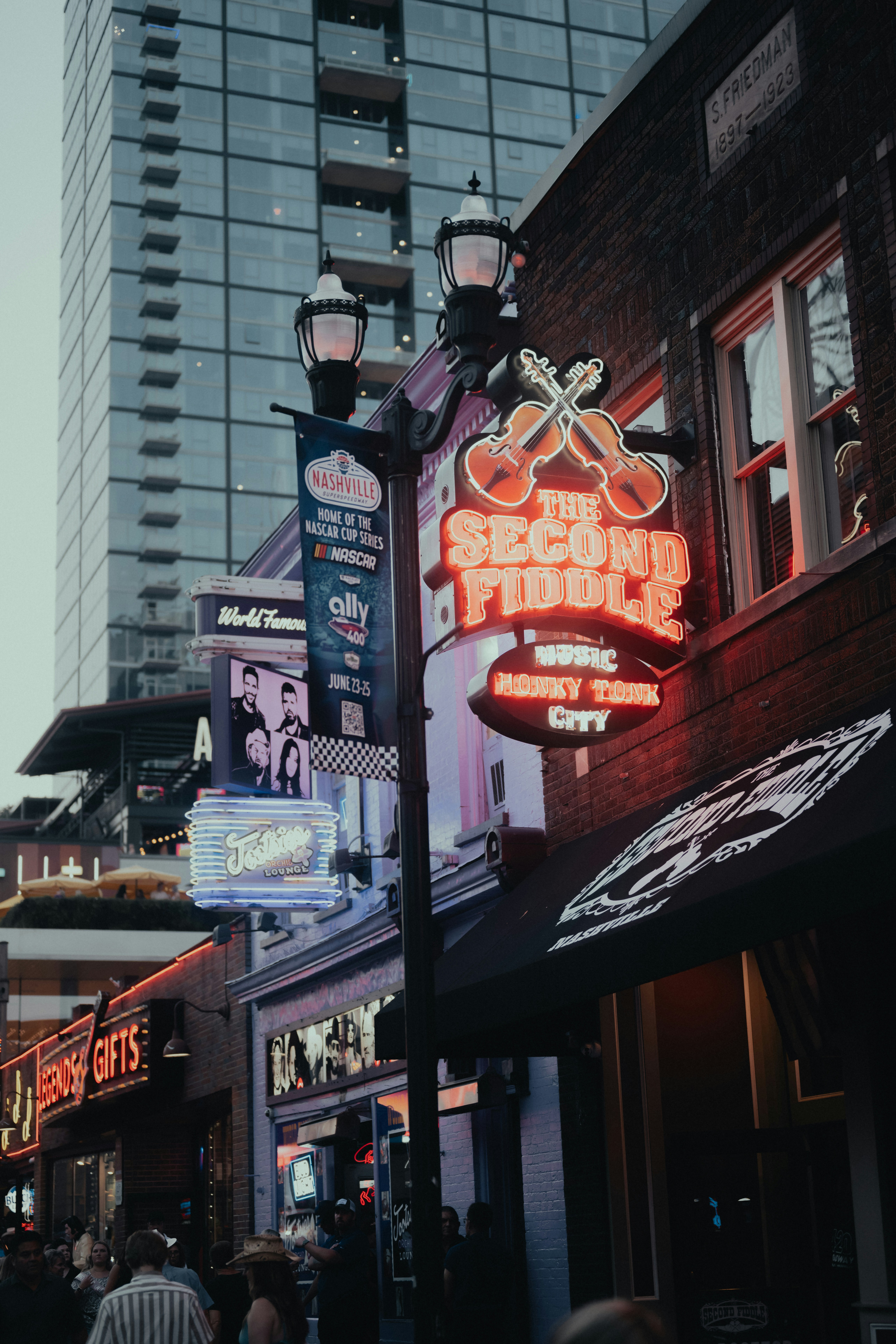 Vibrant neon signs illuminate the bustling streets of Nashville, showcasing the lively atmosphere of music and entertainment. The iconic 'The Second Fiddle' sign stands out amidst the urban backdrop.