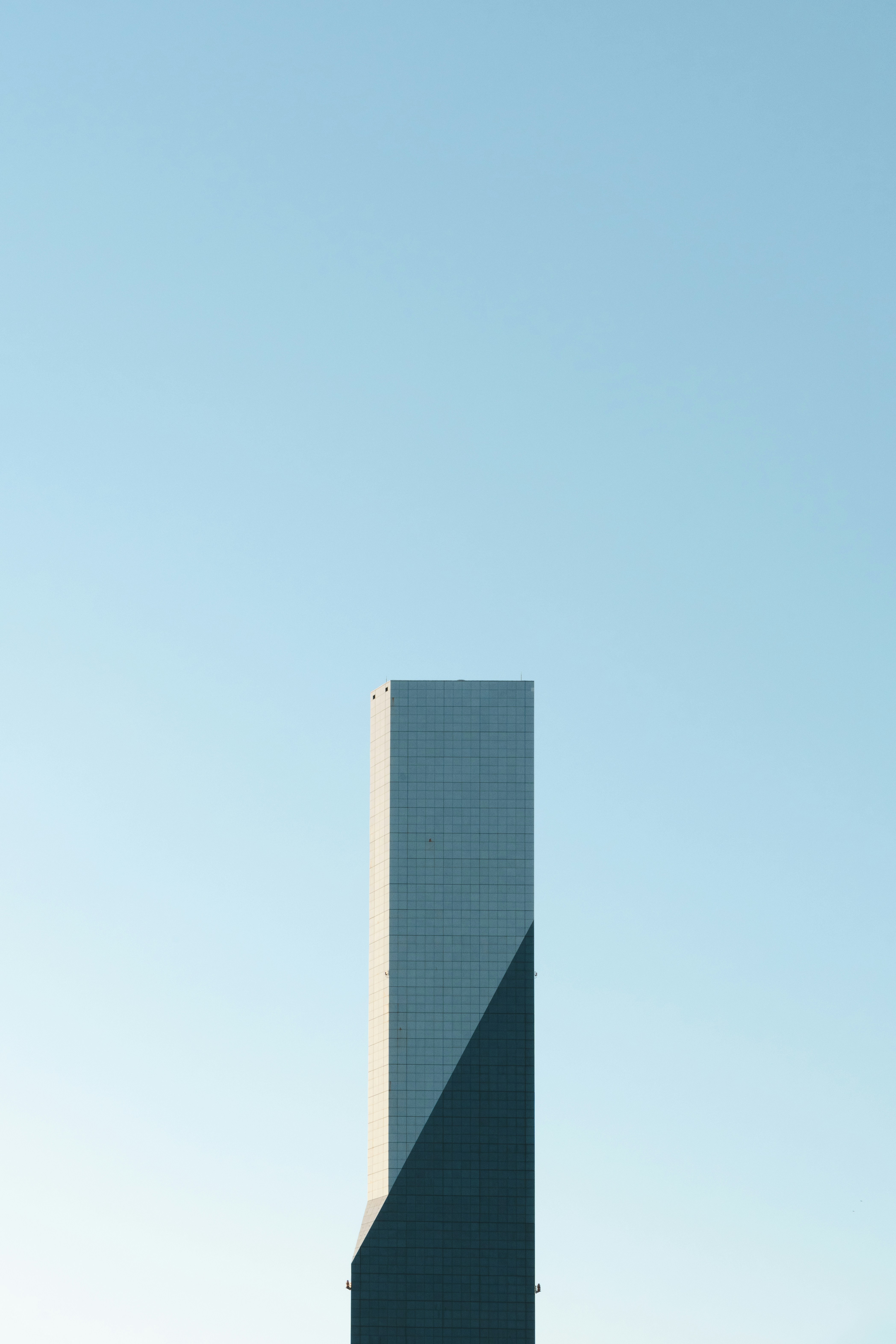 A sleek, modern skyscraper stands against a clear blue sky, showcasing its geometric design and reflective surfaces.