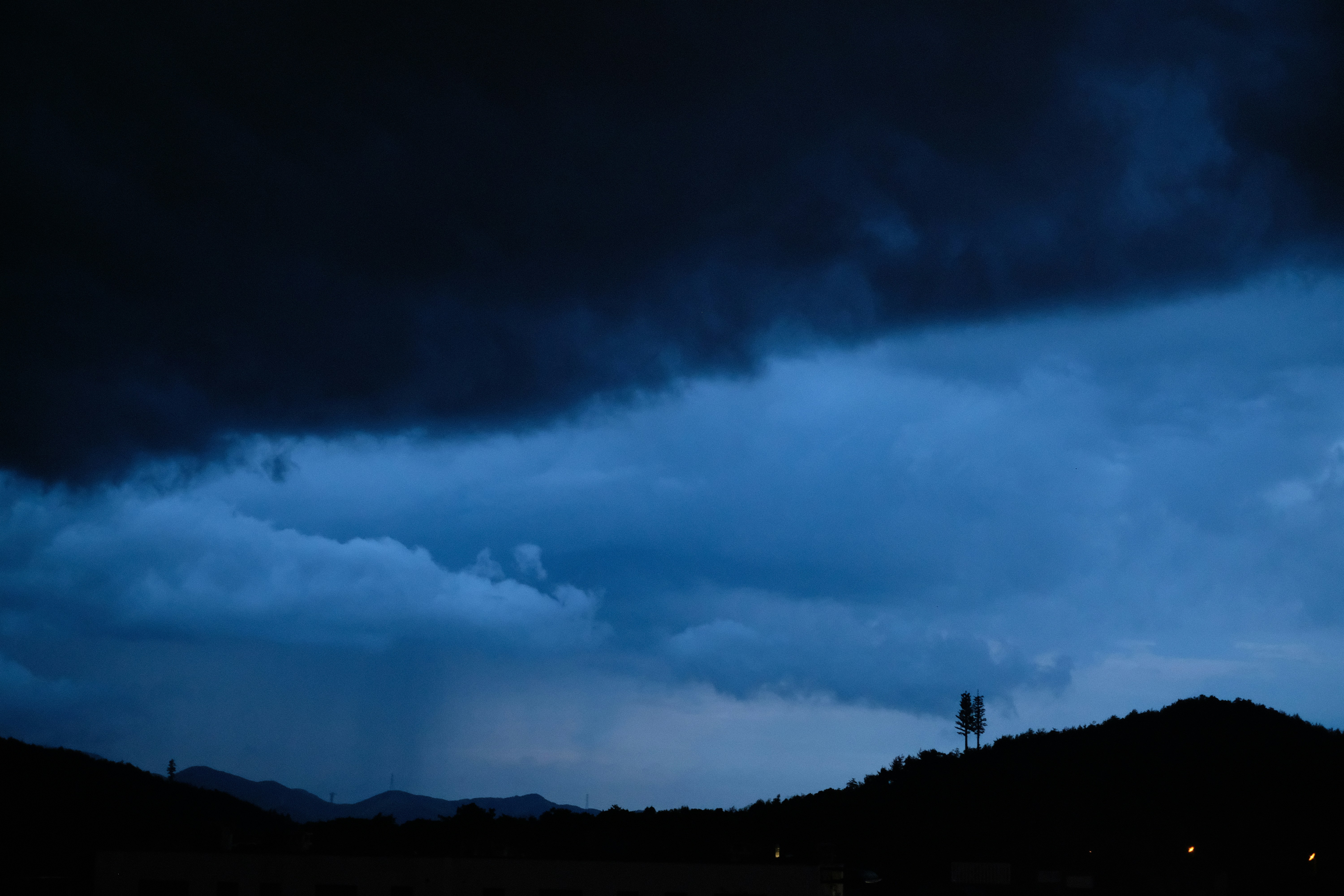 Dark clouds gather ominously above a silhouetted mountain landscape under a twilight sky.