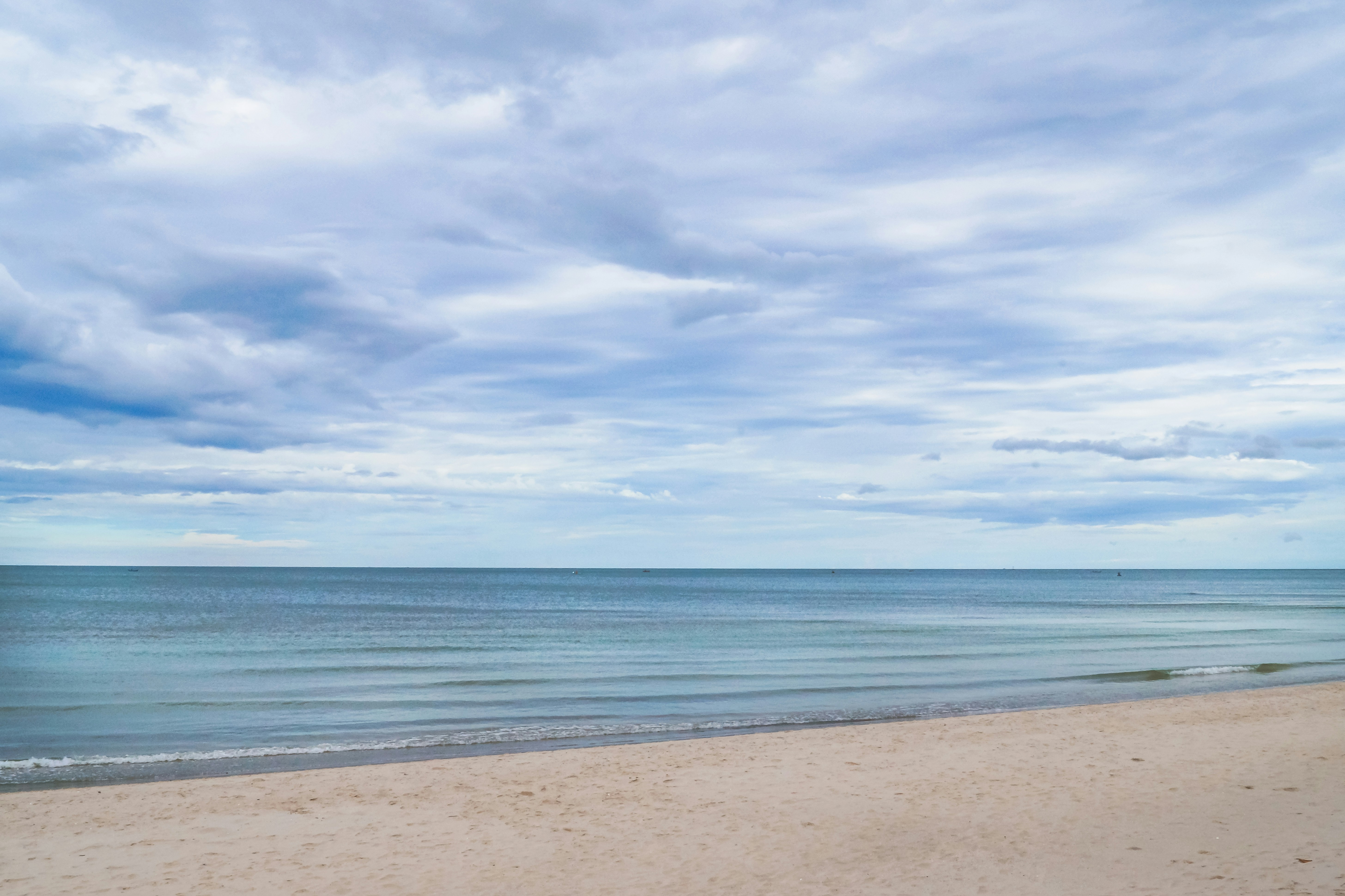 Calm ocean waves gently lap against a sandy beach under a cloudy sky. The tranquil scene invites contemplation.