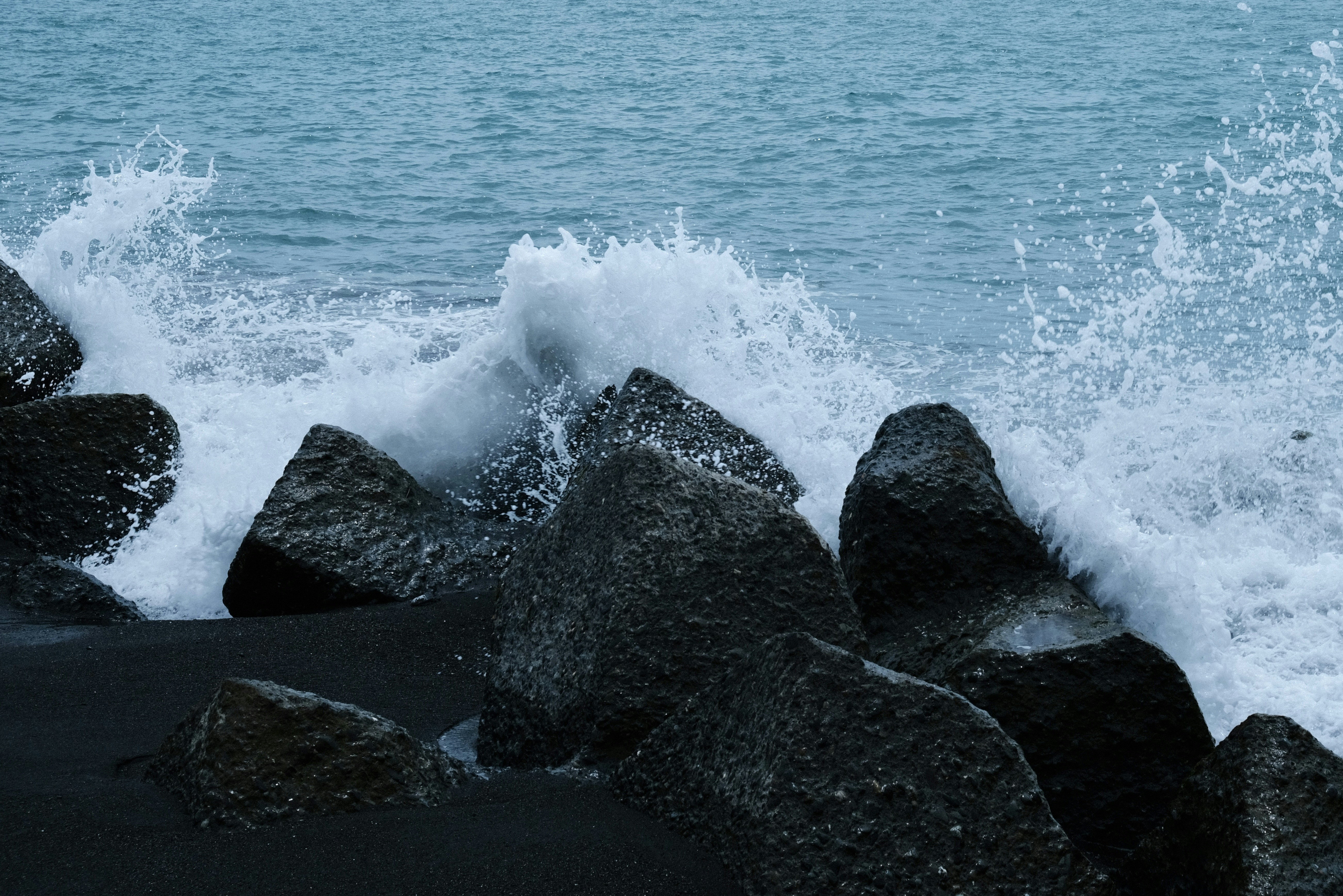 Waves crashing over jagged rocks on a dark sandy shore.