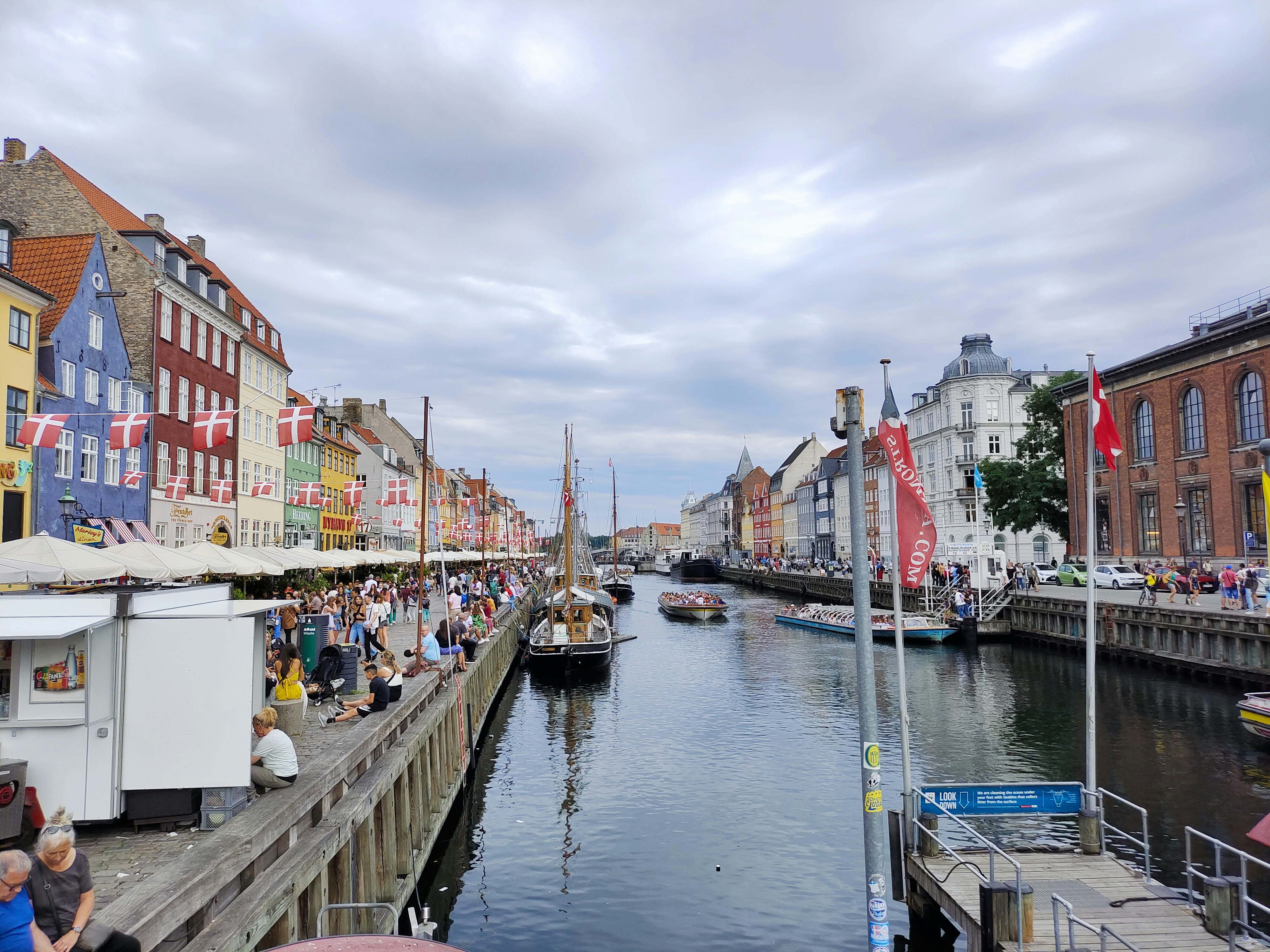 Photograph of Nyhavn canal in Copenhagen with pastel townhouses, moored boats, and pedestrians along the quay.