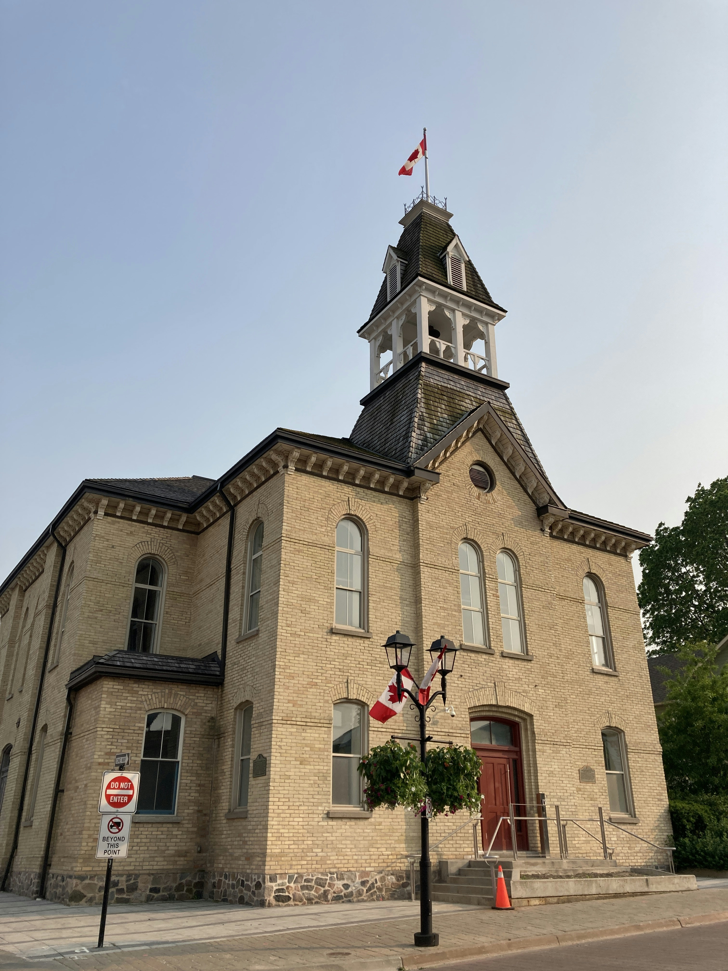 Historic building featuring a prominent clock tower and Canadian flags, set against a clear sky.