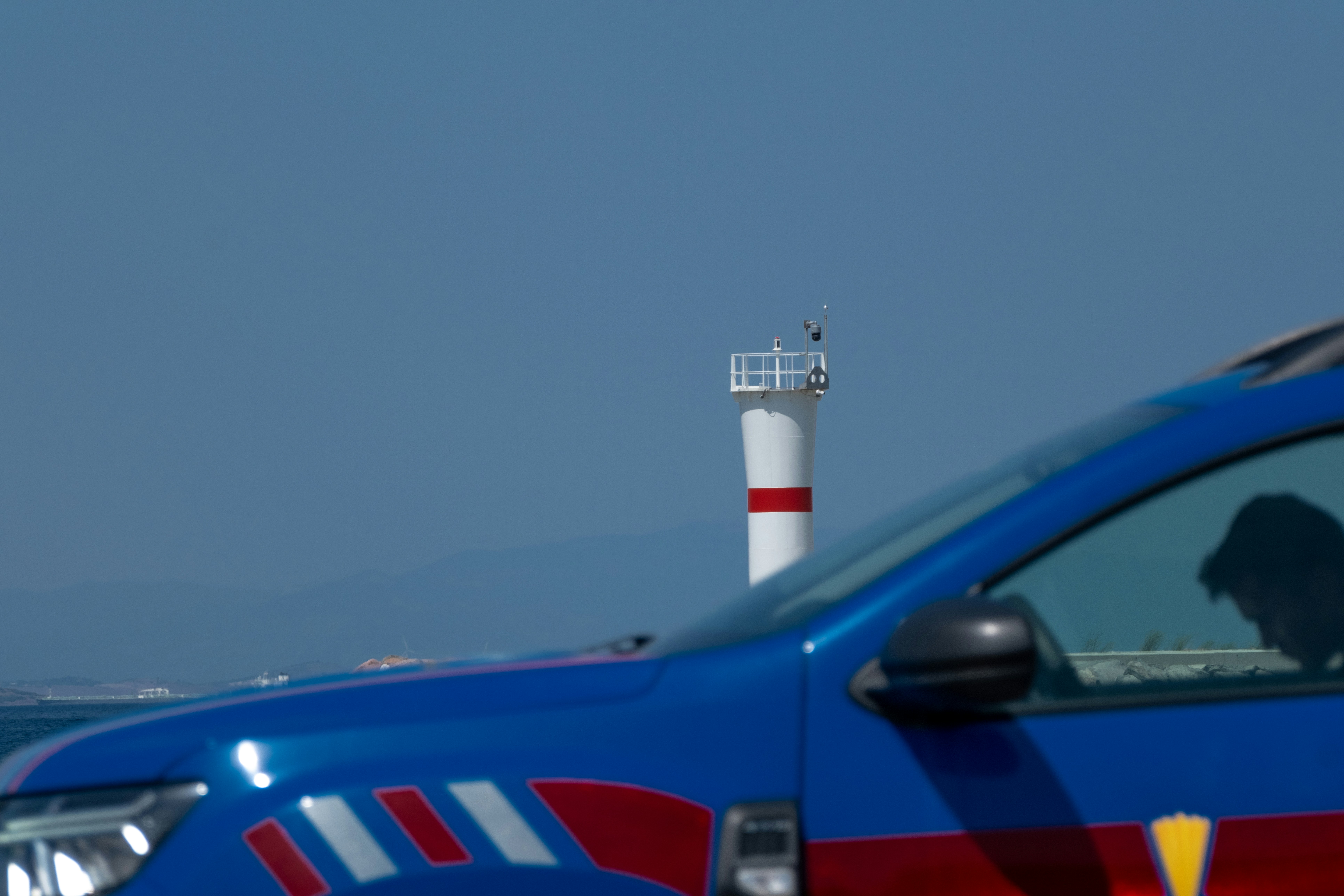 Lighthouse in the Distance Framed by a Racing Blue Car