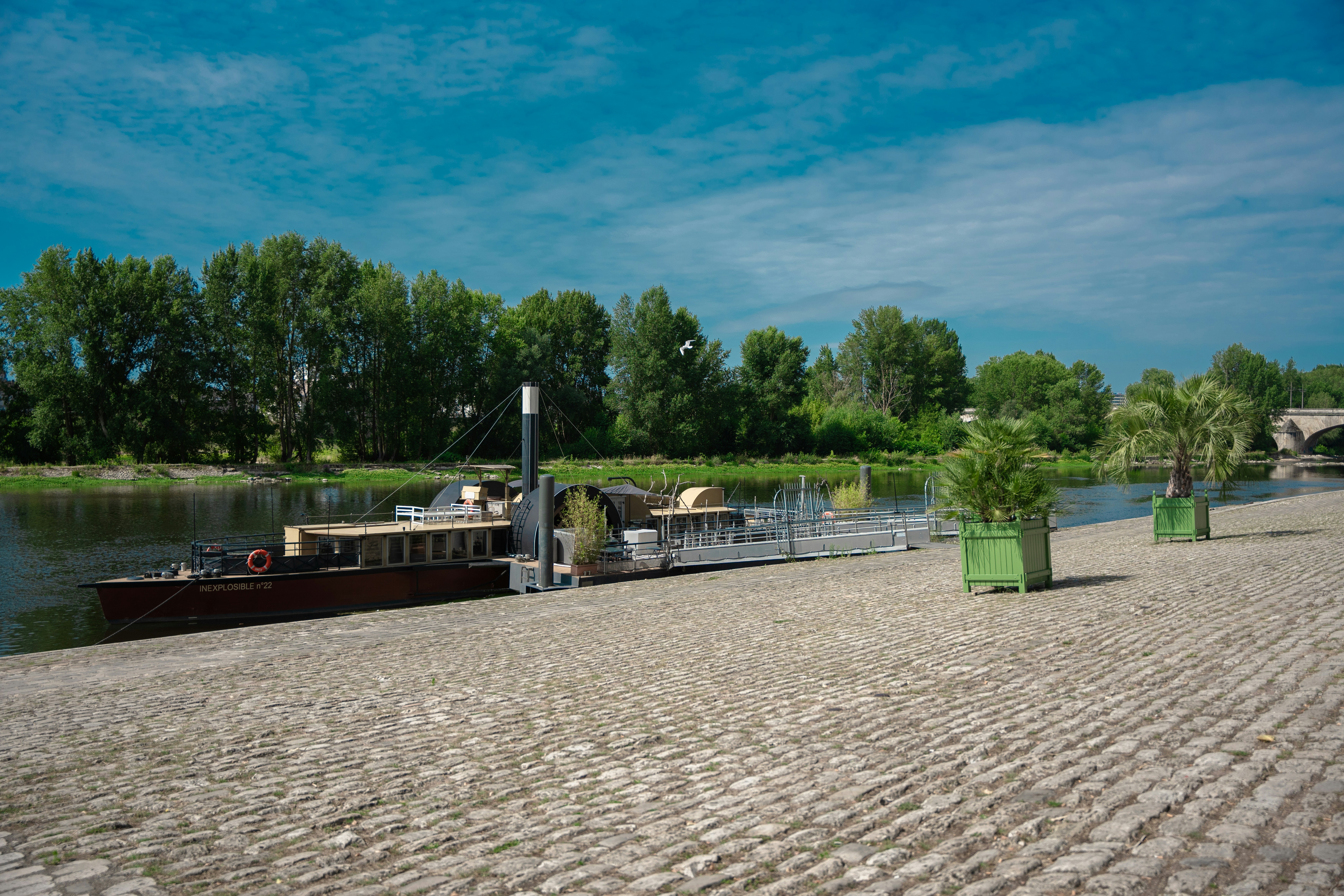 Sunlit Riverfront Docked Boat by a Cobblestone Quay