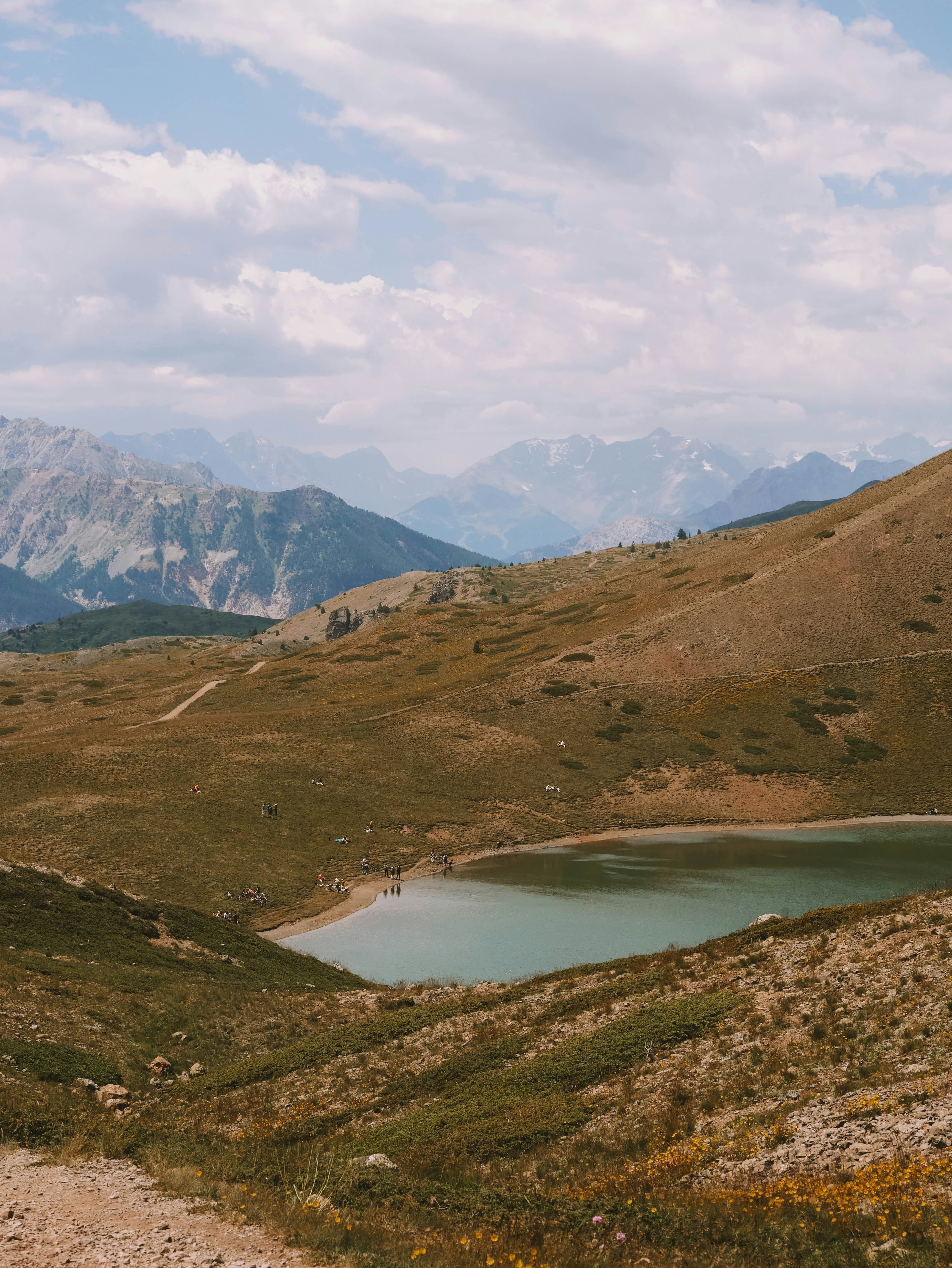 Mountain landscape with a tranquil lake surrounded by rolling hills under a partly cloudy sky.