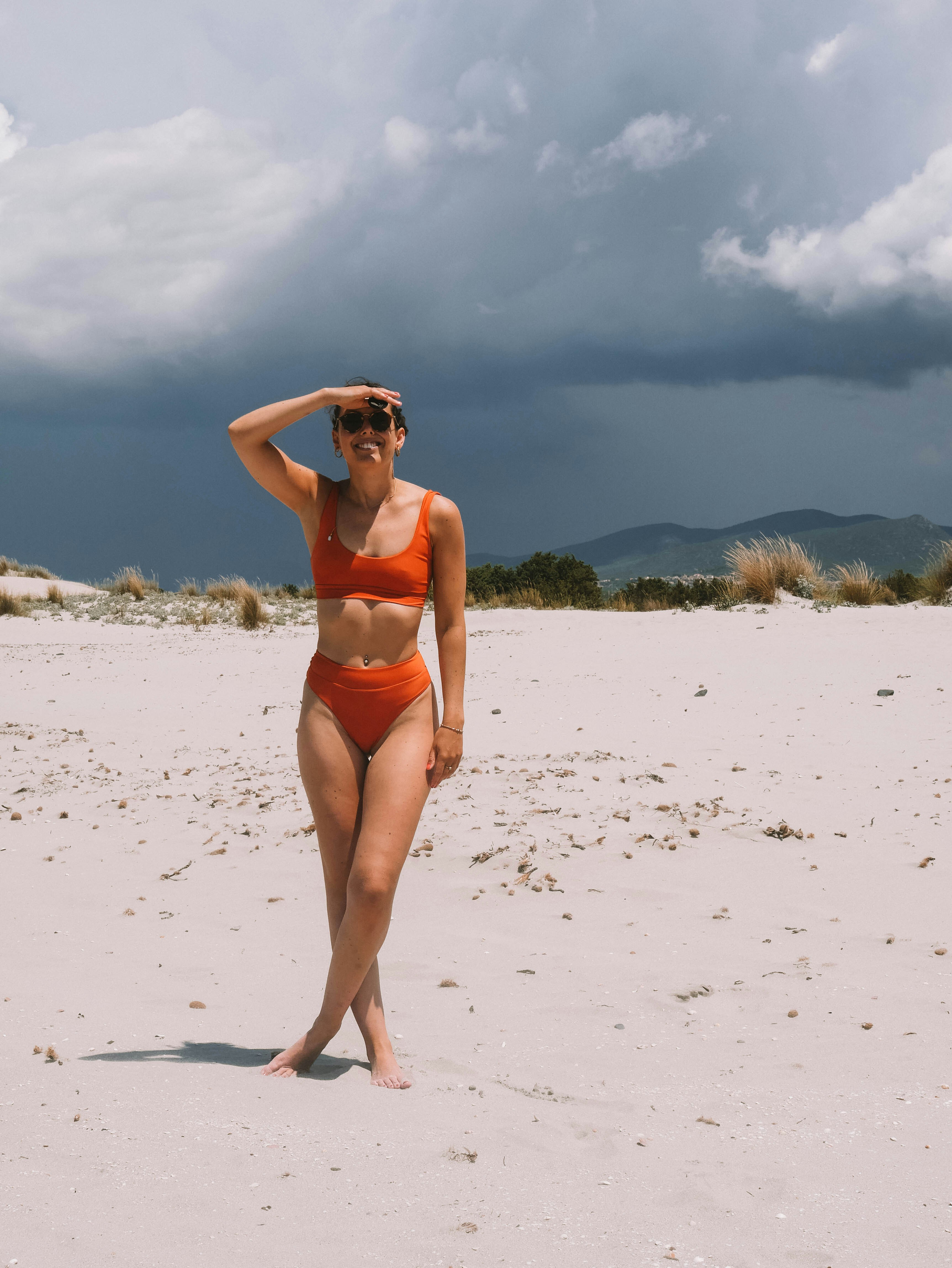 Girl posing on the beach with clouds in the background.