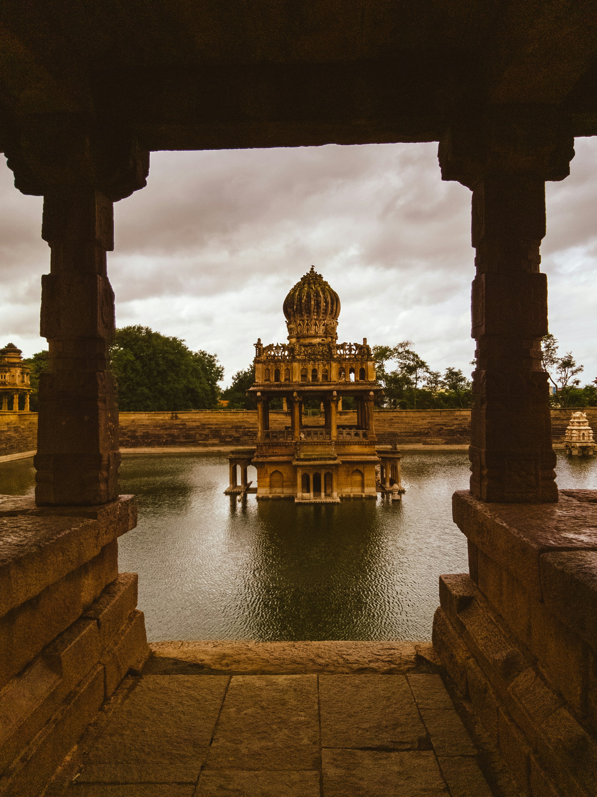 Intricate temple island framed by arches over reflective water, centered in a tranquil courtyard scene.