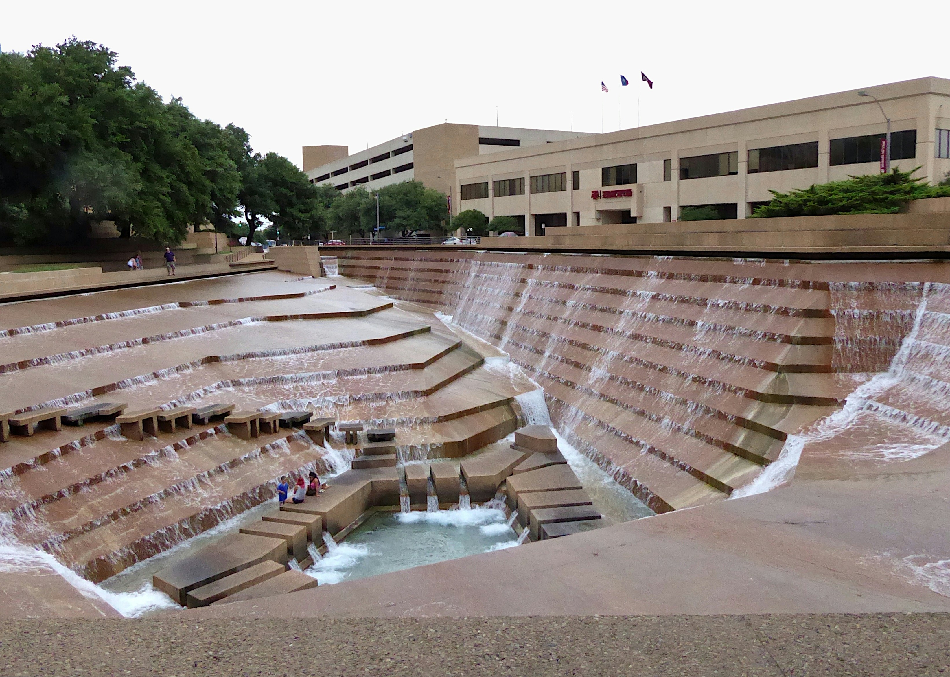 Terraced urban waterfall with people exploring its cascading steps.