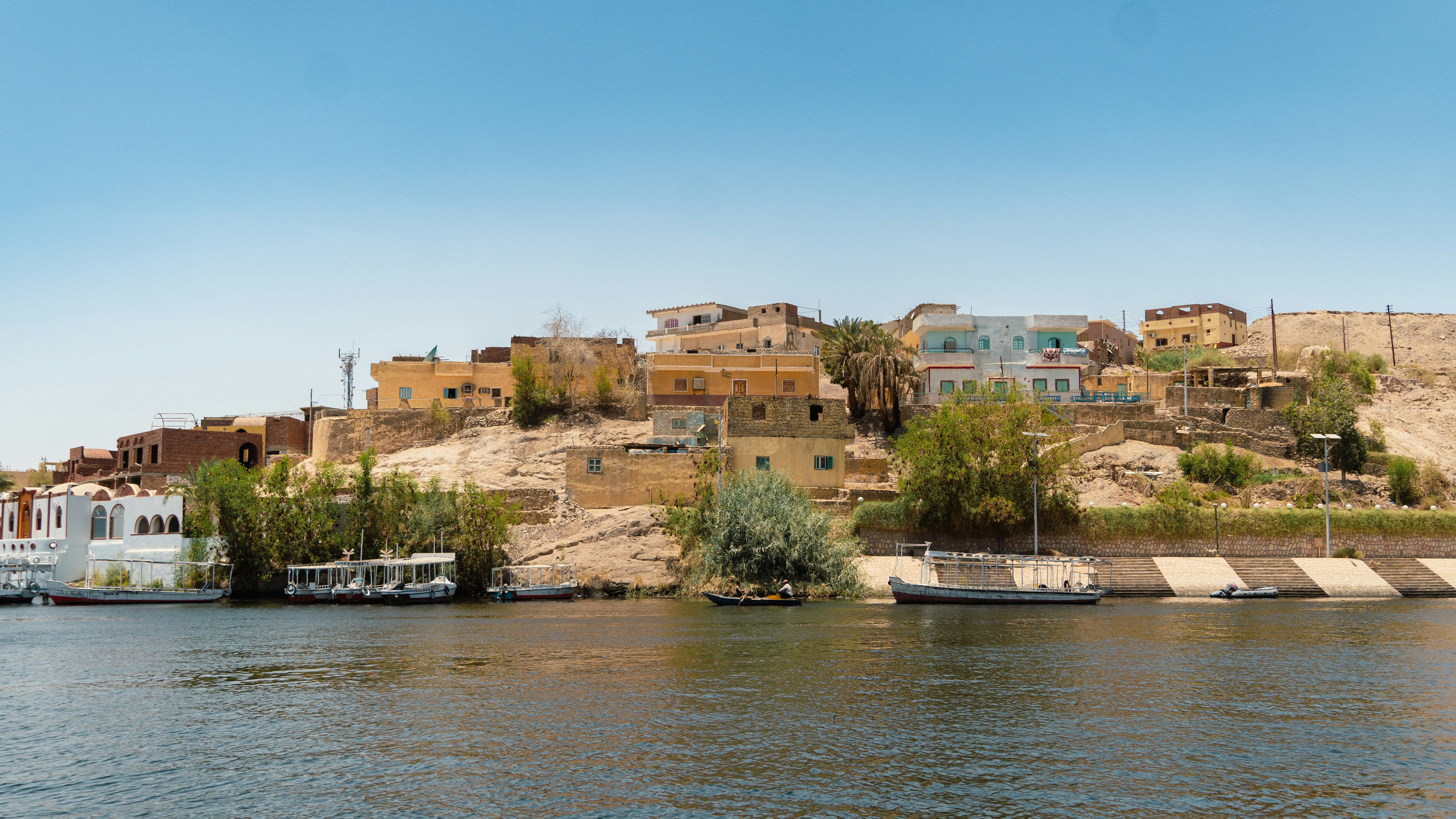 Colorful houses perched on a sandy hillside overlooking a serene river, showcasing a blend of nature and architecture.