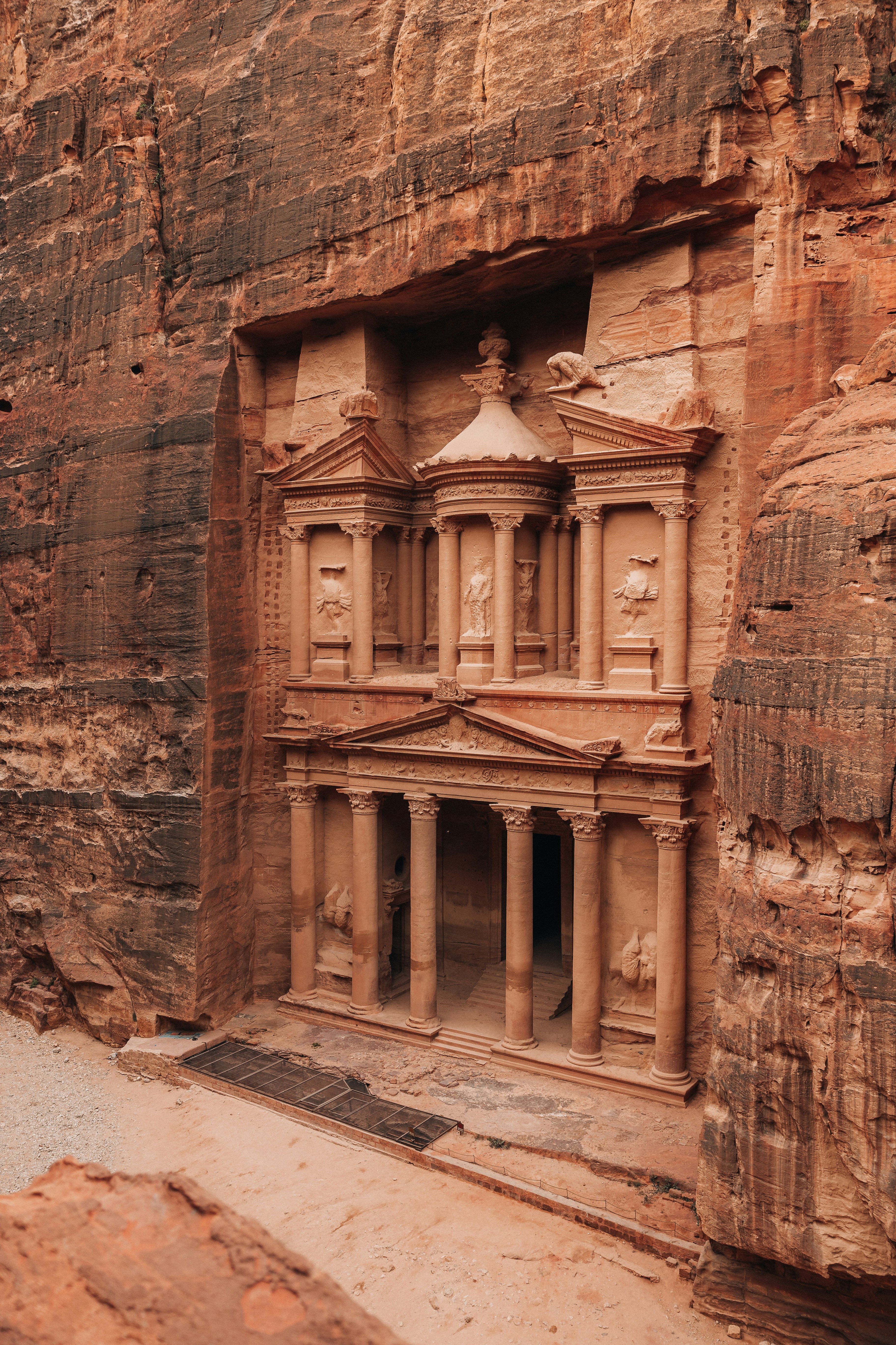 Intricately carved façade of the Treasury at Petra, surrounded by towering rock formations. The architectural details reflect the grandeur of a bygone era.