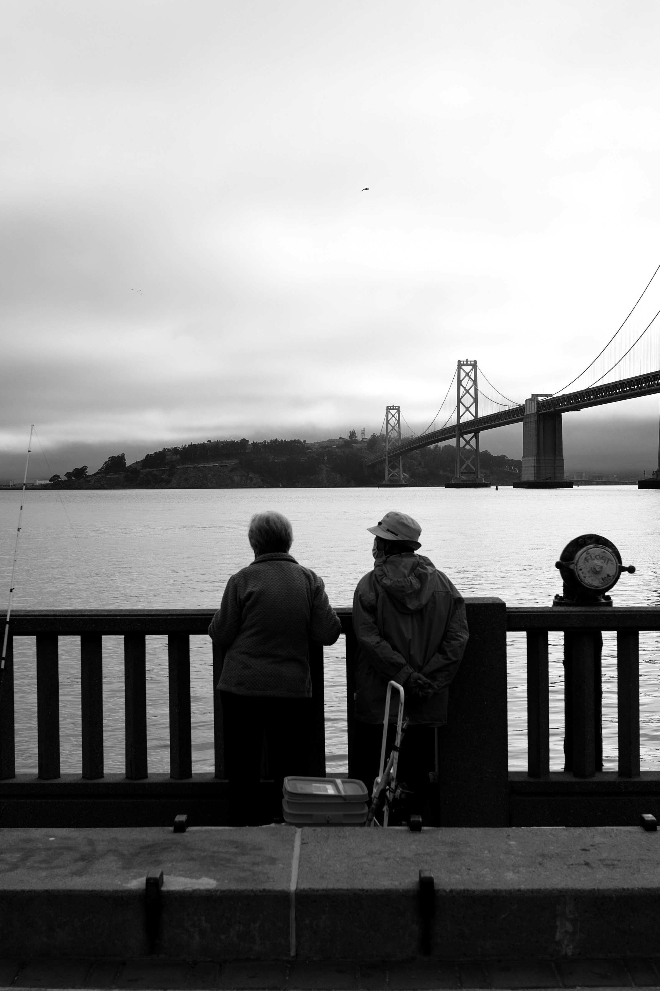 Two silhouetted observers at the railing with a distant bridge and water