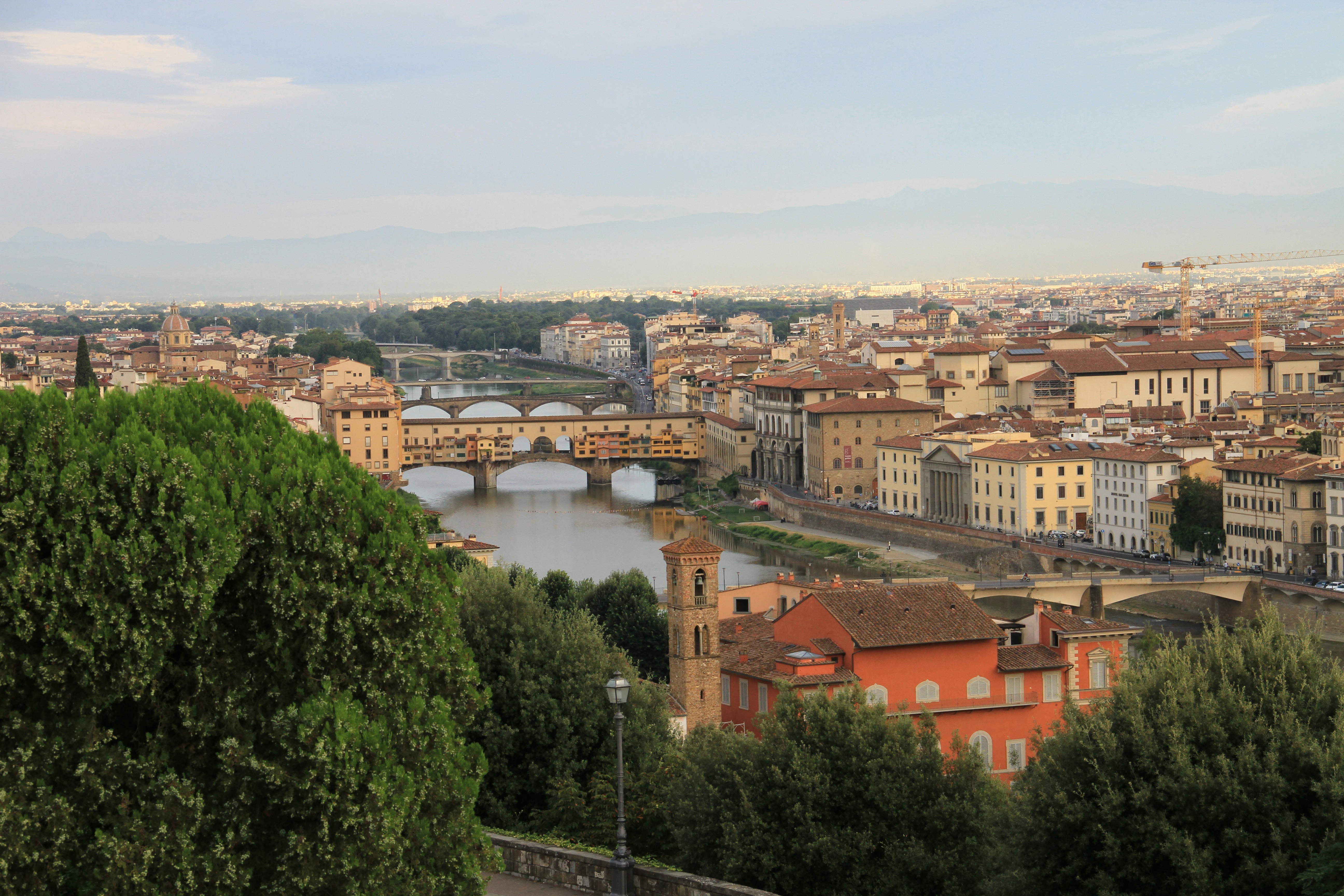View of Florence showcasing the iconic Ponte Vecchio bridge over the Arno River, framed by lush greenery and historical buildings.