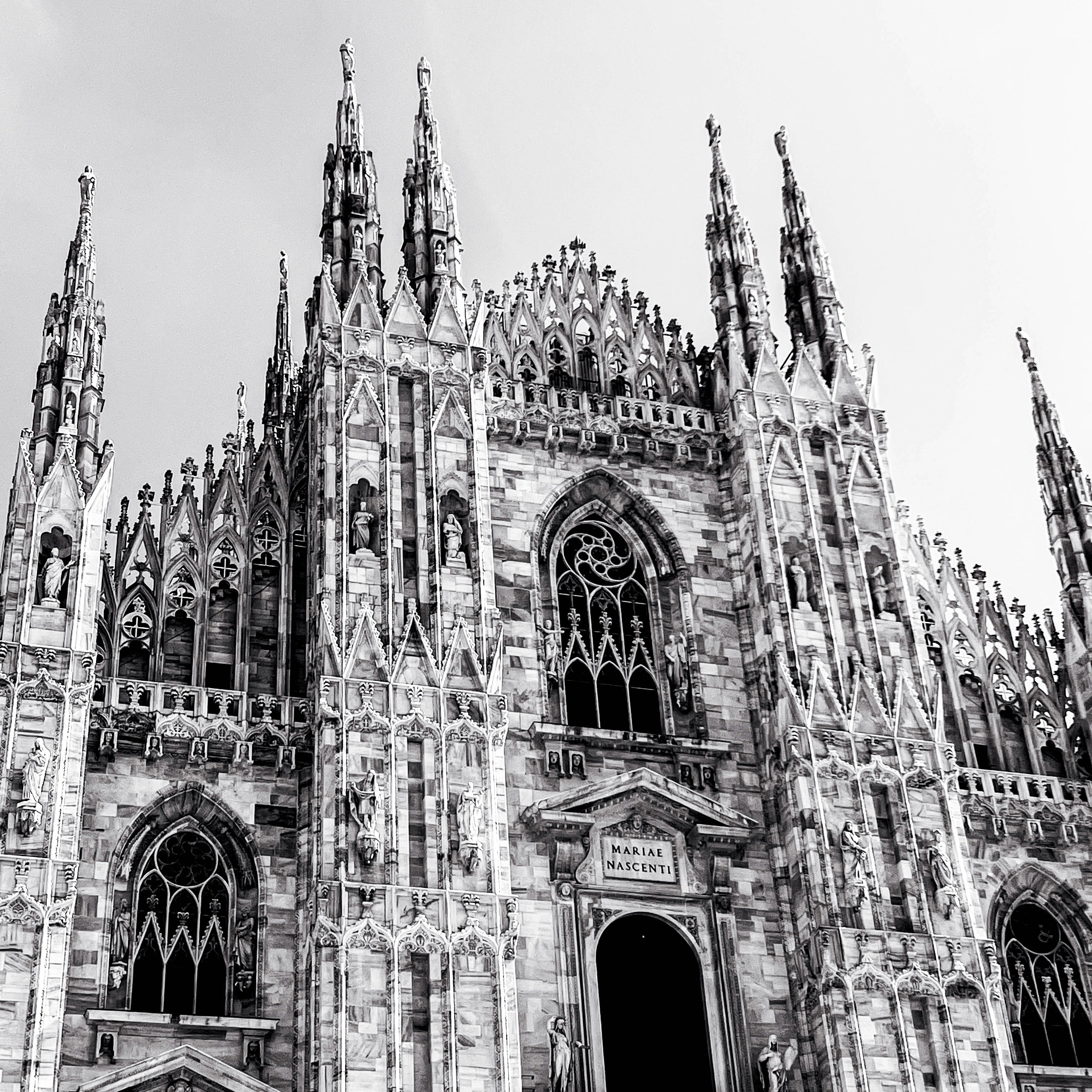 Intricate Gothic architecture of a grand cathedral, showcasing detailed spires and ornate stonework under a cloudy sky.
