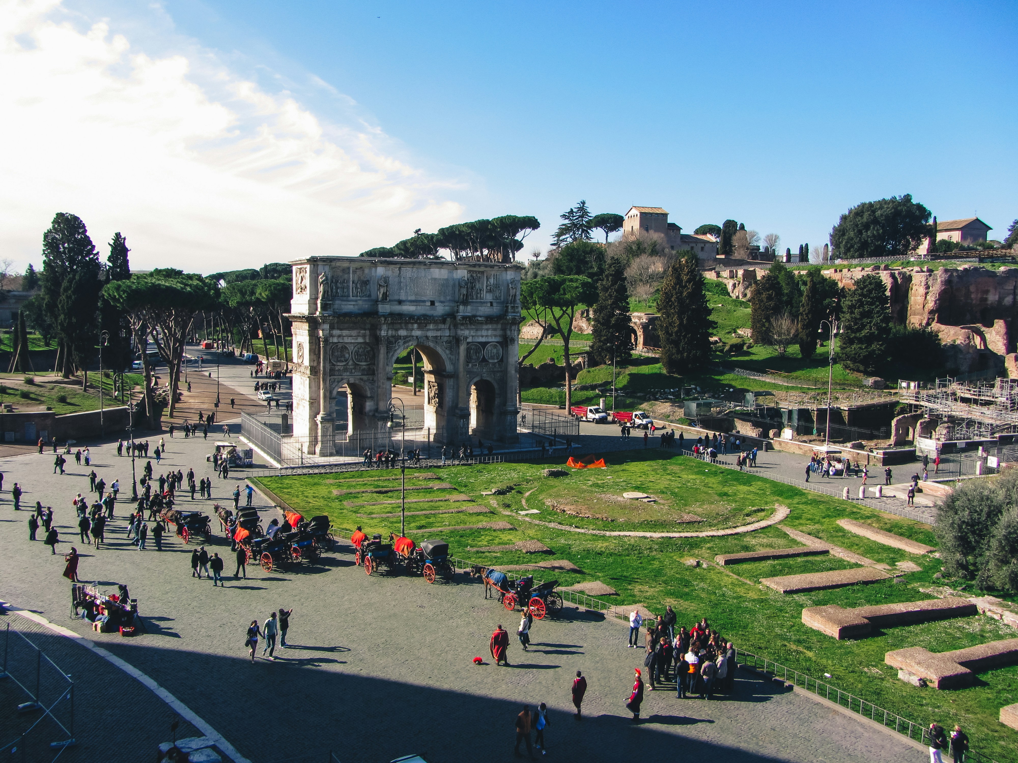 Arch of Constantine surrounded by visitors and green landscape under a clear blue sky.