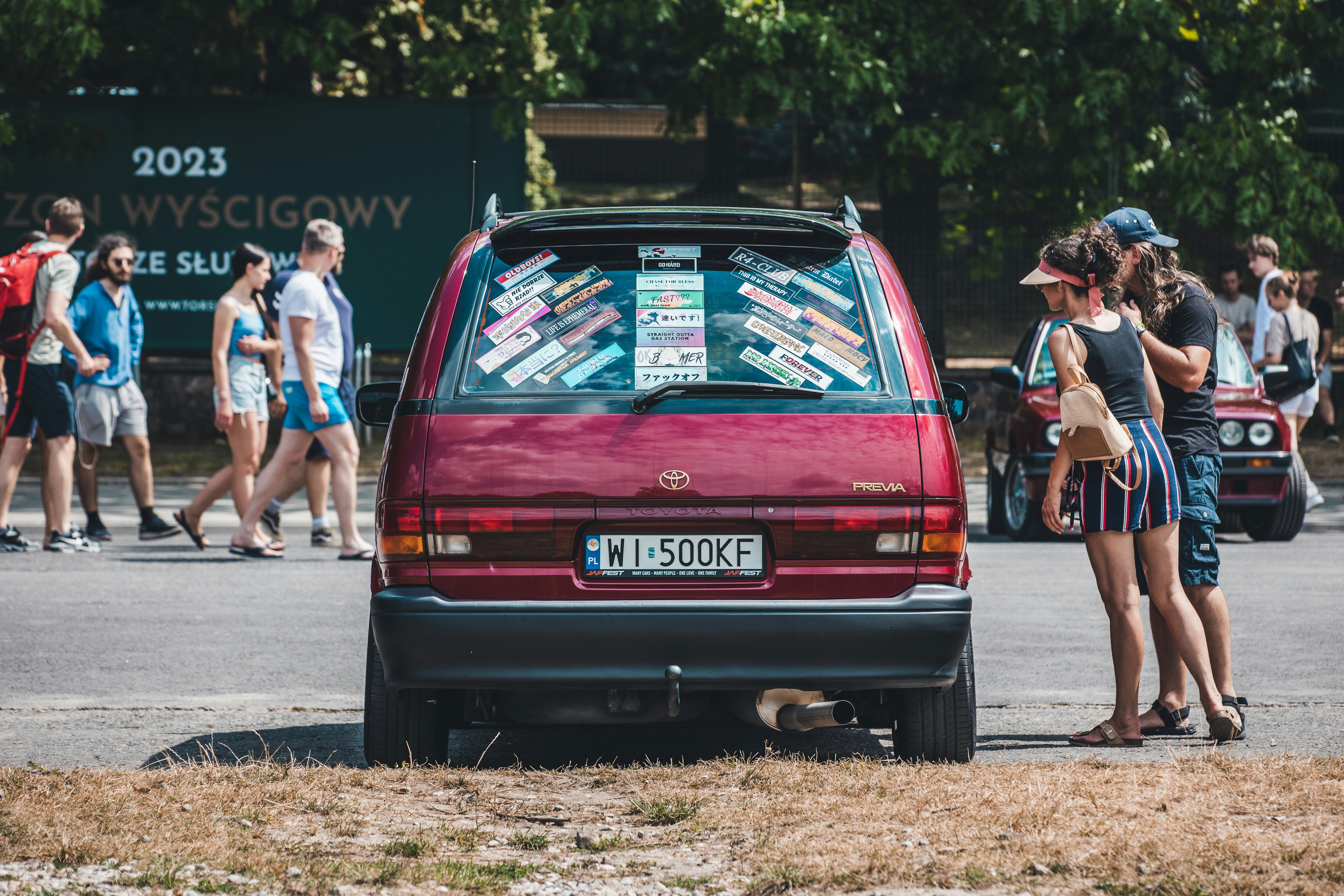 Stickered Spotlight: A Red Hatchback Surrounded by a Weekend Car Show Crowd