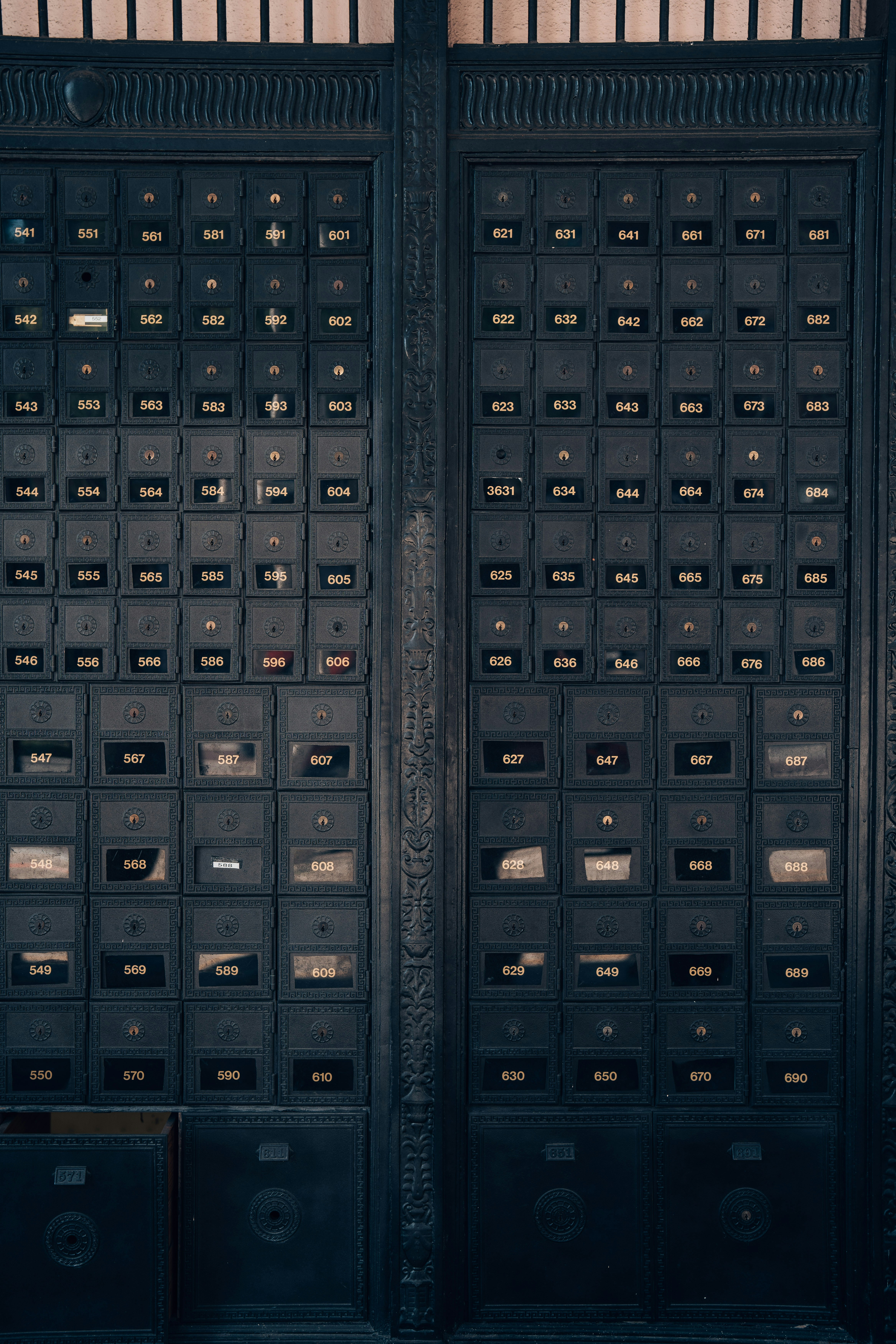 A captivating image of vintage mailboxes, arranged in neat rows, captured in a dimly lit corridor. The deep navy blue and black tones of the mailboxes create a nostalgic atmosphere, while the soft, ambient lighting highlights the intricate details and numbers on each box. This image evokes a sense of history and mystery, making it visually striking.