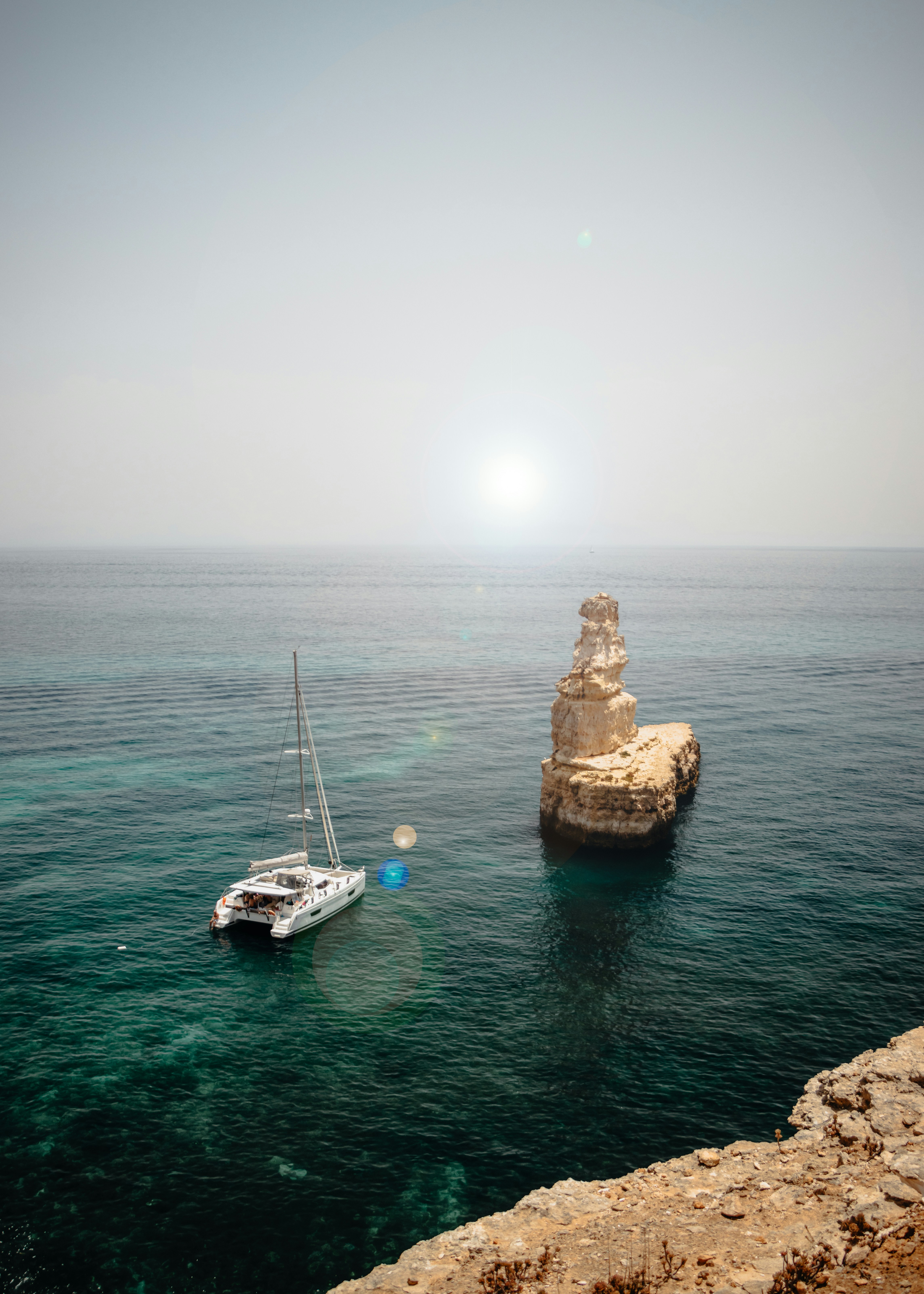 A sailboat floating in the ocean next to a rock formation photo – Free ...