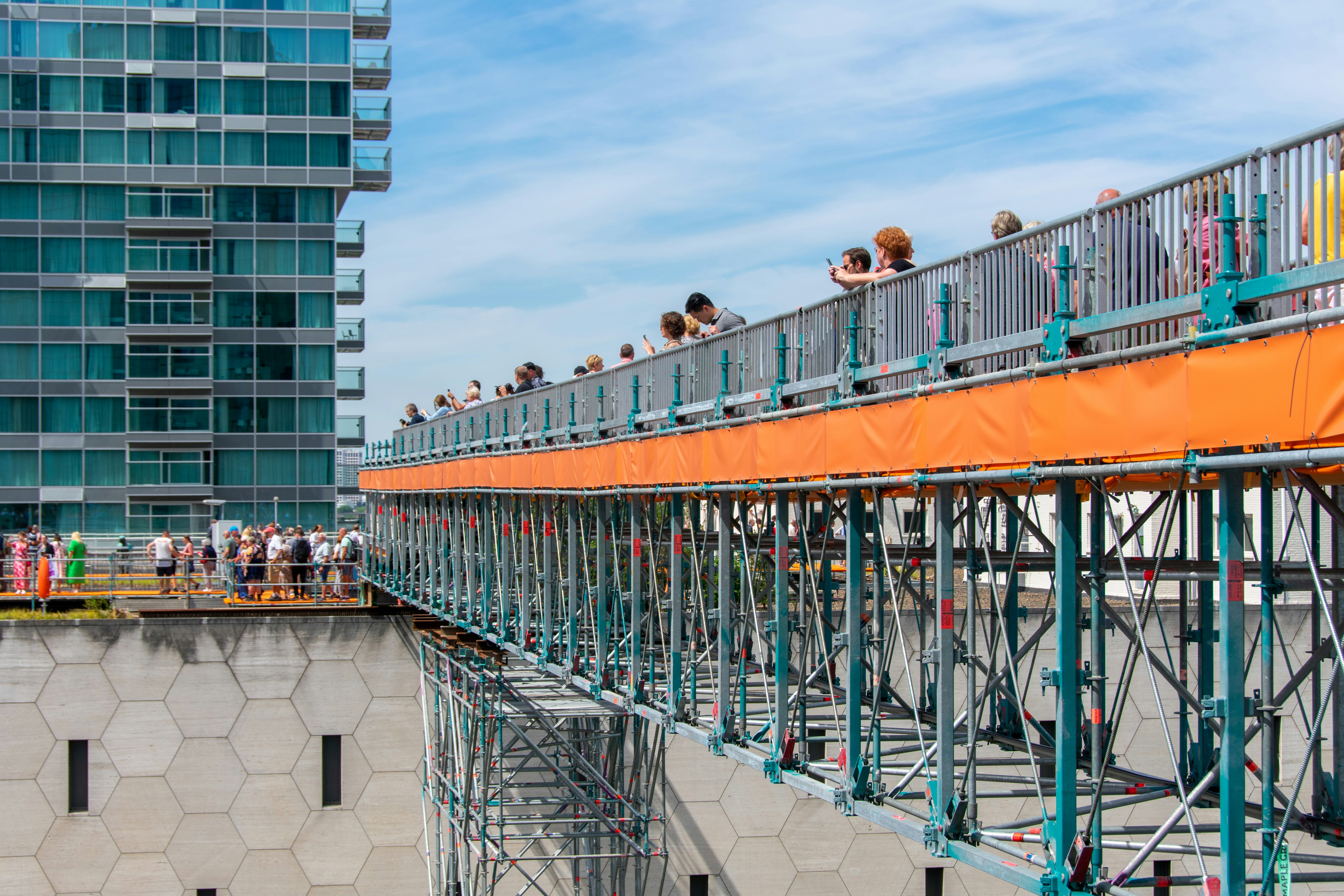 Skywalk in Motion: Crowds Cross an Orange-Strip Skybridge Above a Concrete Atrium