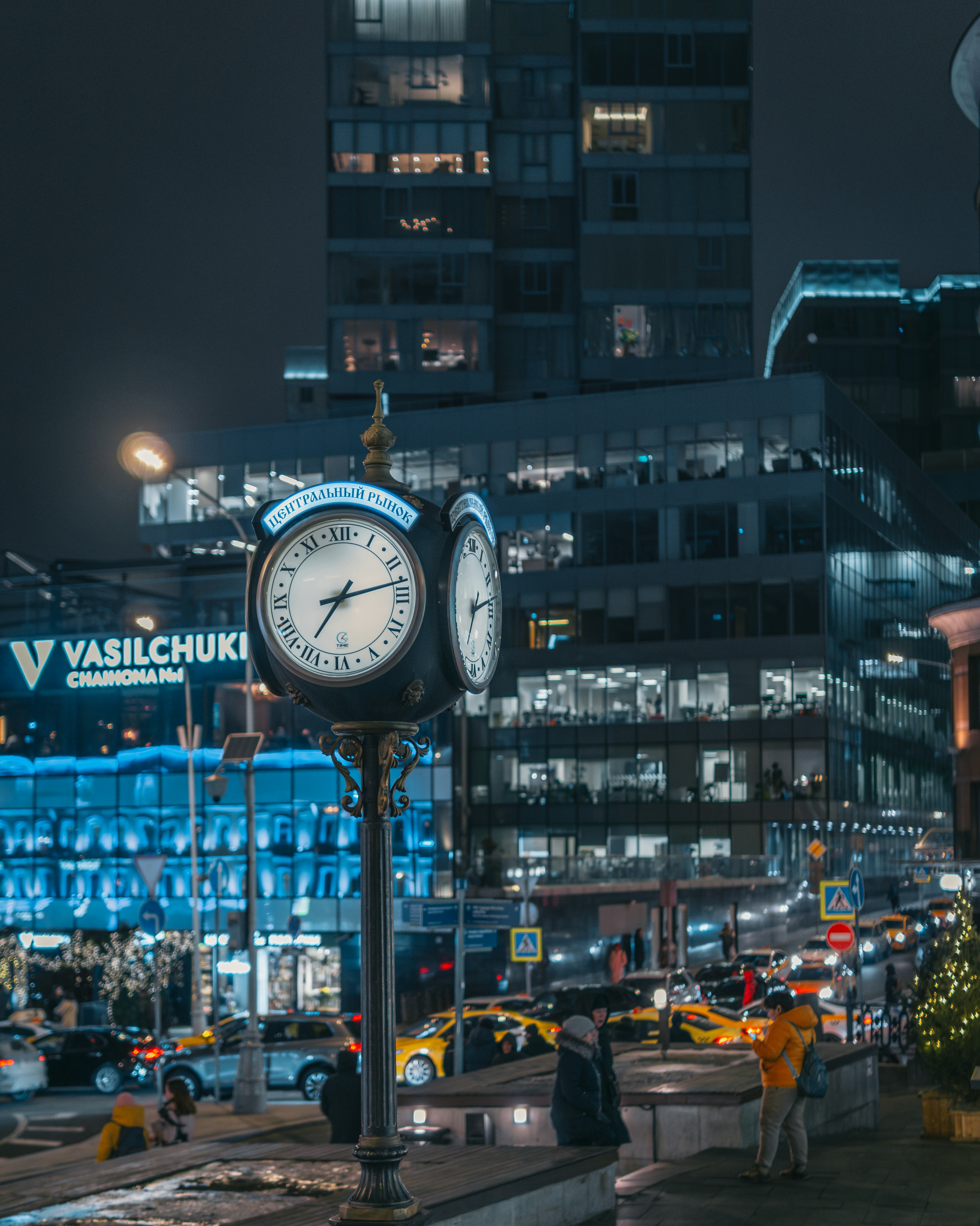 Timekeeper in Neon Blue: A Night Street Clock Amid Urban Glass