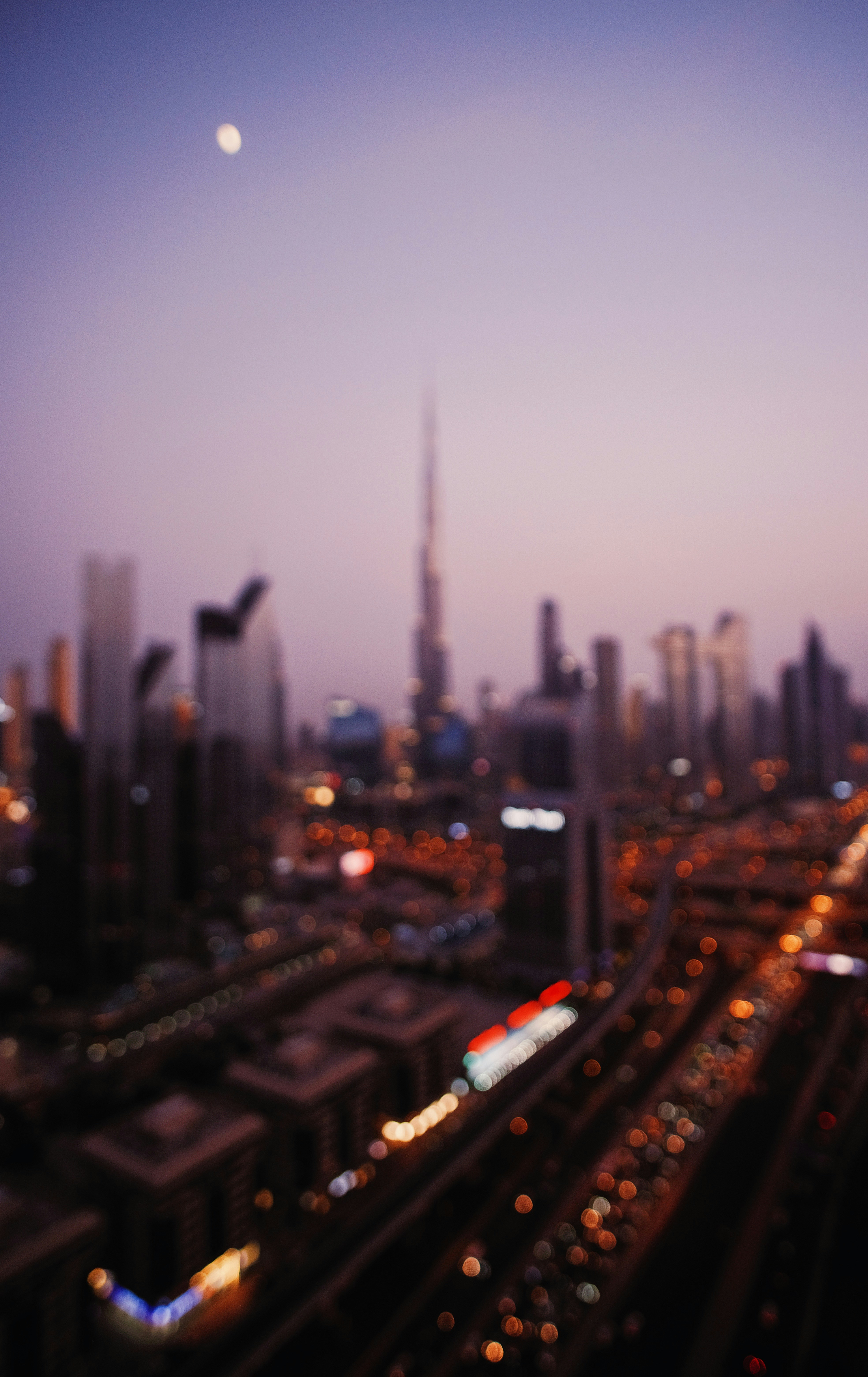A blurred city skyline at twilight, with the iconic Burj Khalifa emerging against a gradient sky and soft city lights below.
