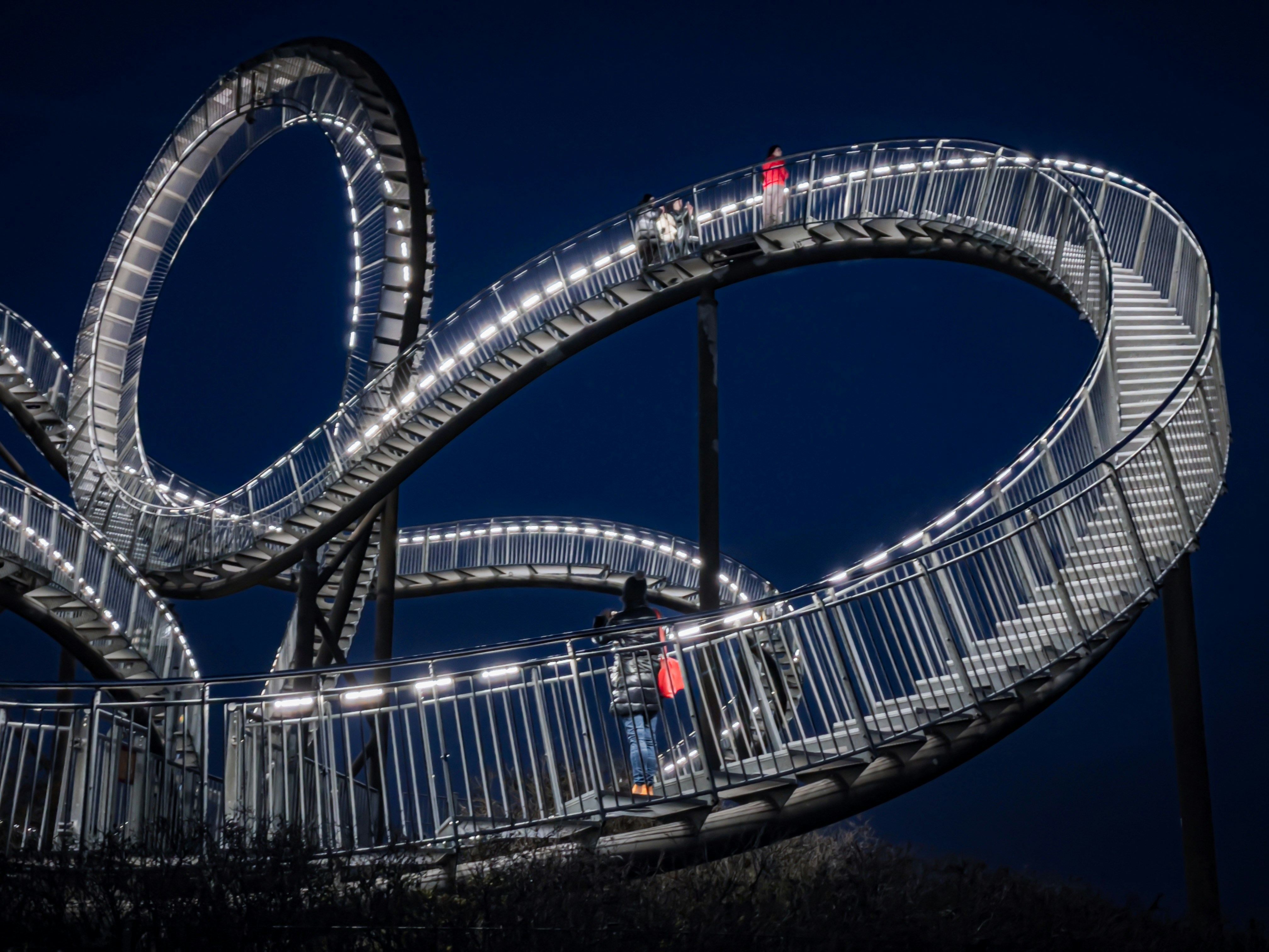 Neon Coil at Night: Pedestrians Thread a Spiraling Steel Loop
