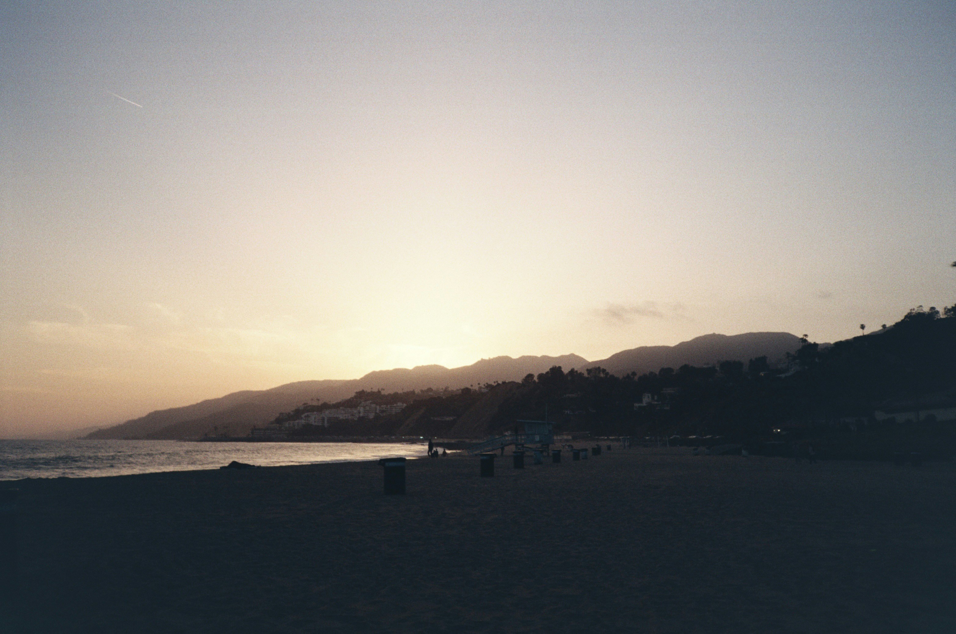 Sundown on a quiet beach with silhouetted hills and a distant village along the shore.