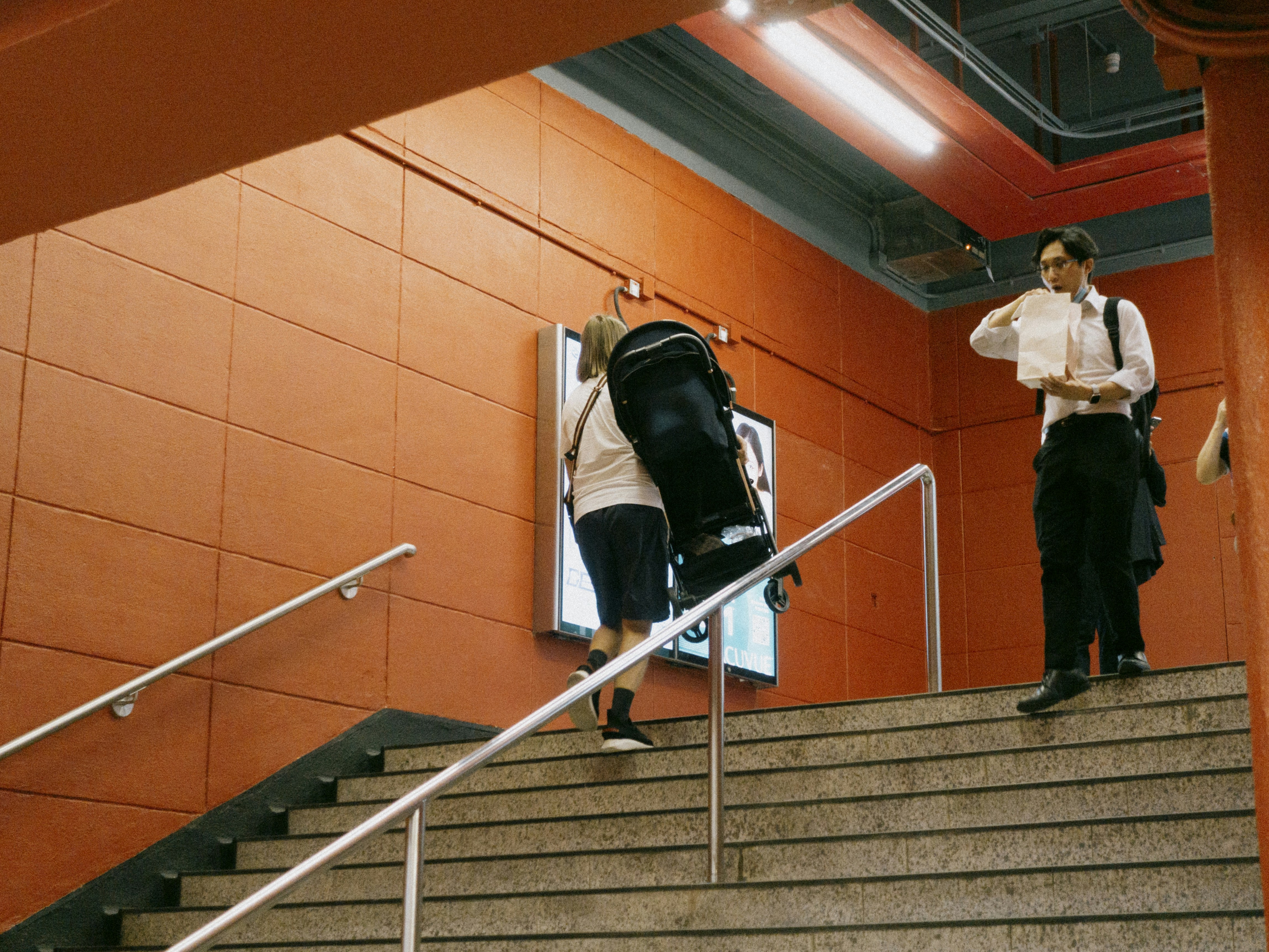 Stairwell Pause: A commuter watches as a stroller climbs the landing