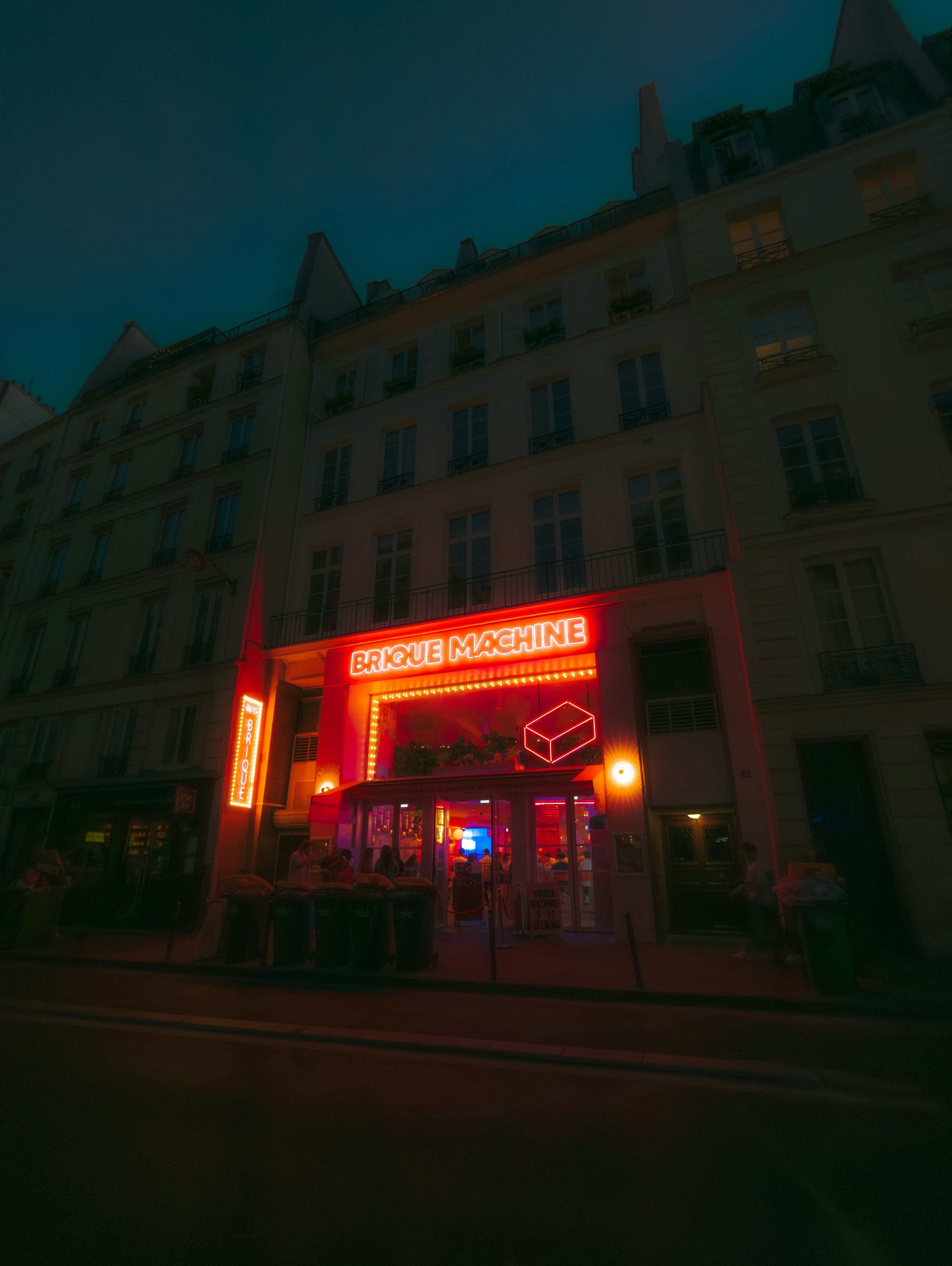 Nighttime street photograph of a neon-red storefront with warm interior lighting visible through the glass.