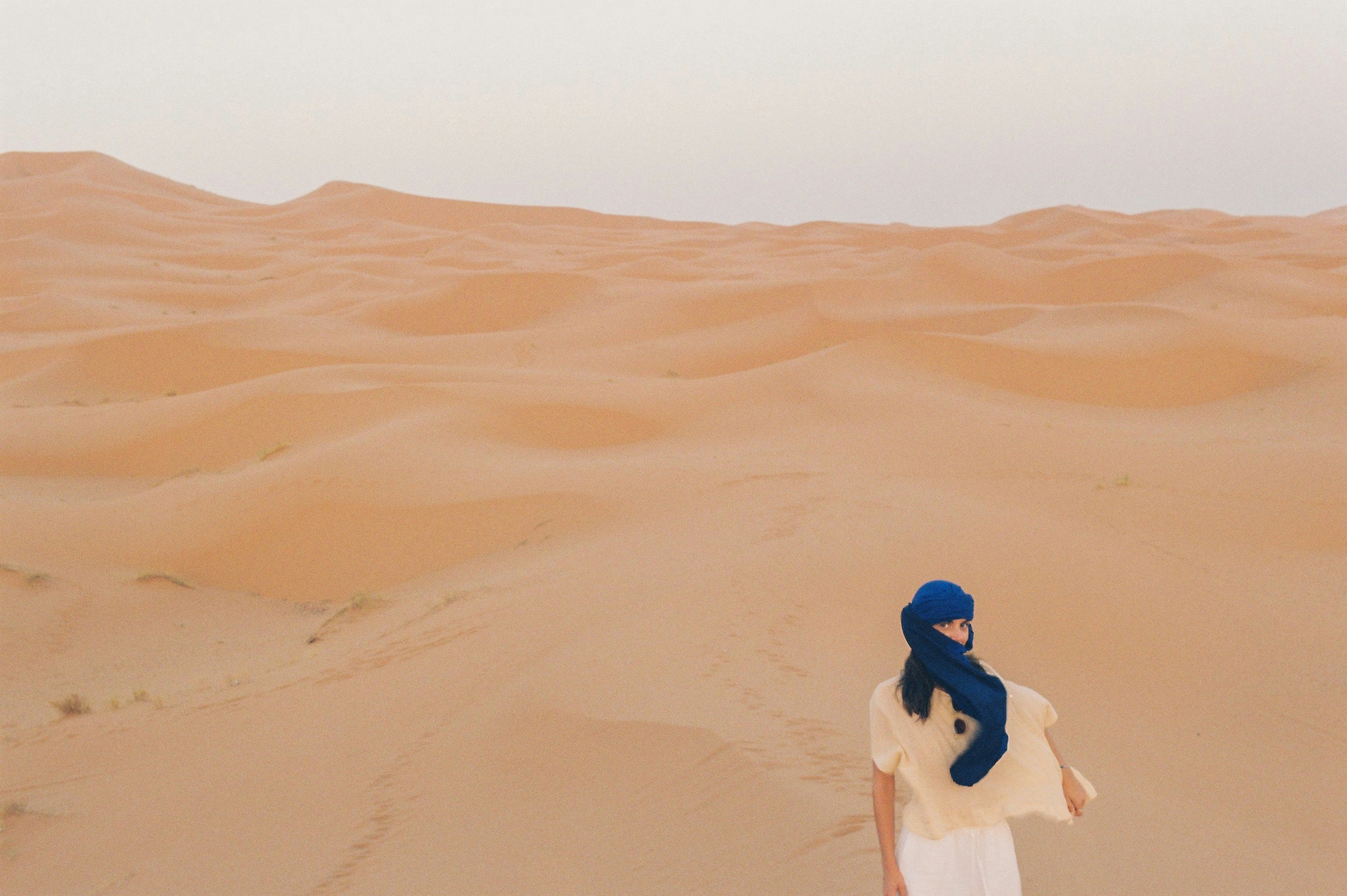 Blue-scarfed figure traversing an endless amber dune sea