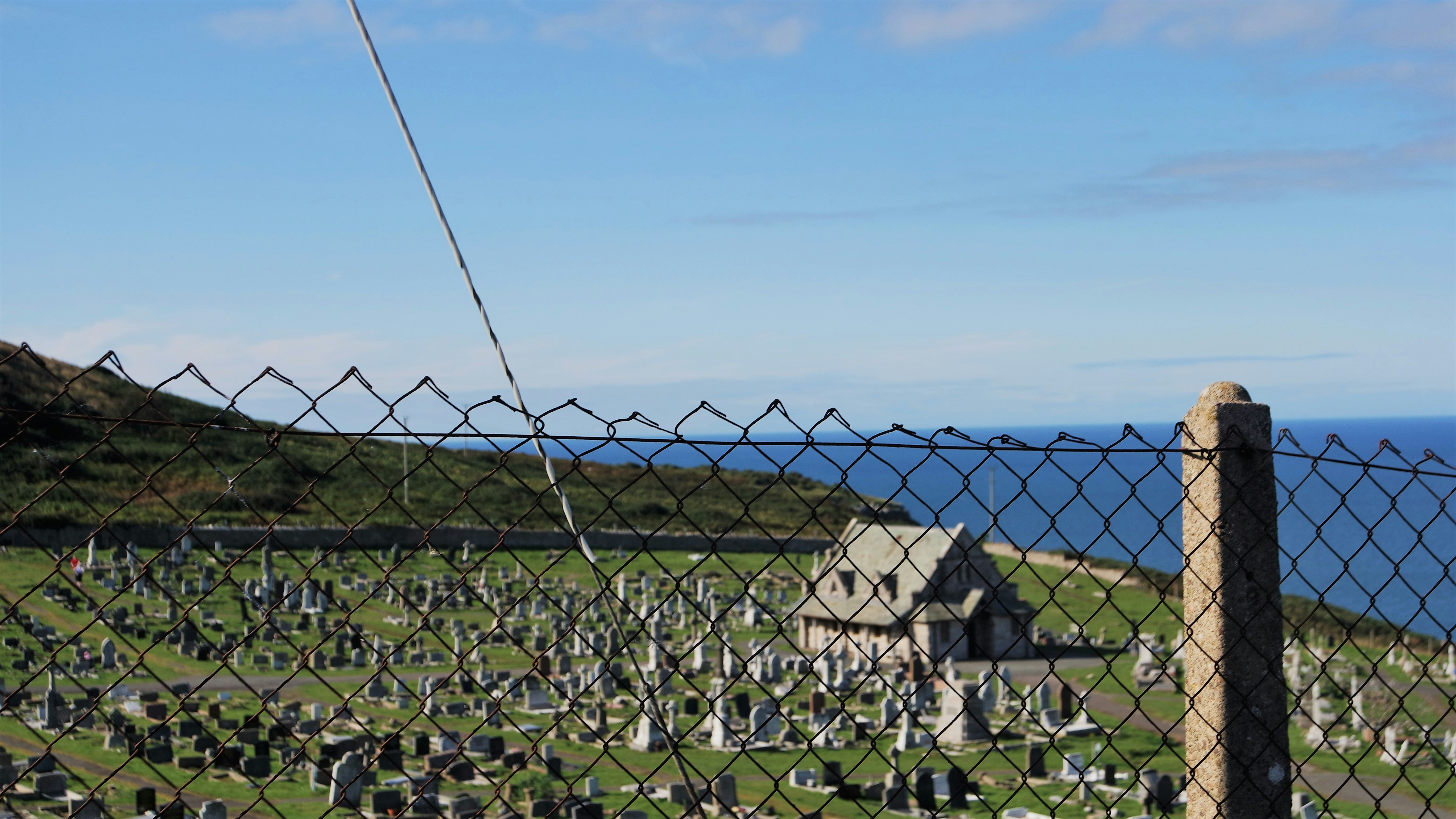 A cemetery with a house in the background behind a chain link fence ...