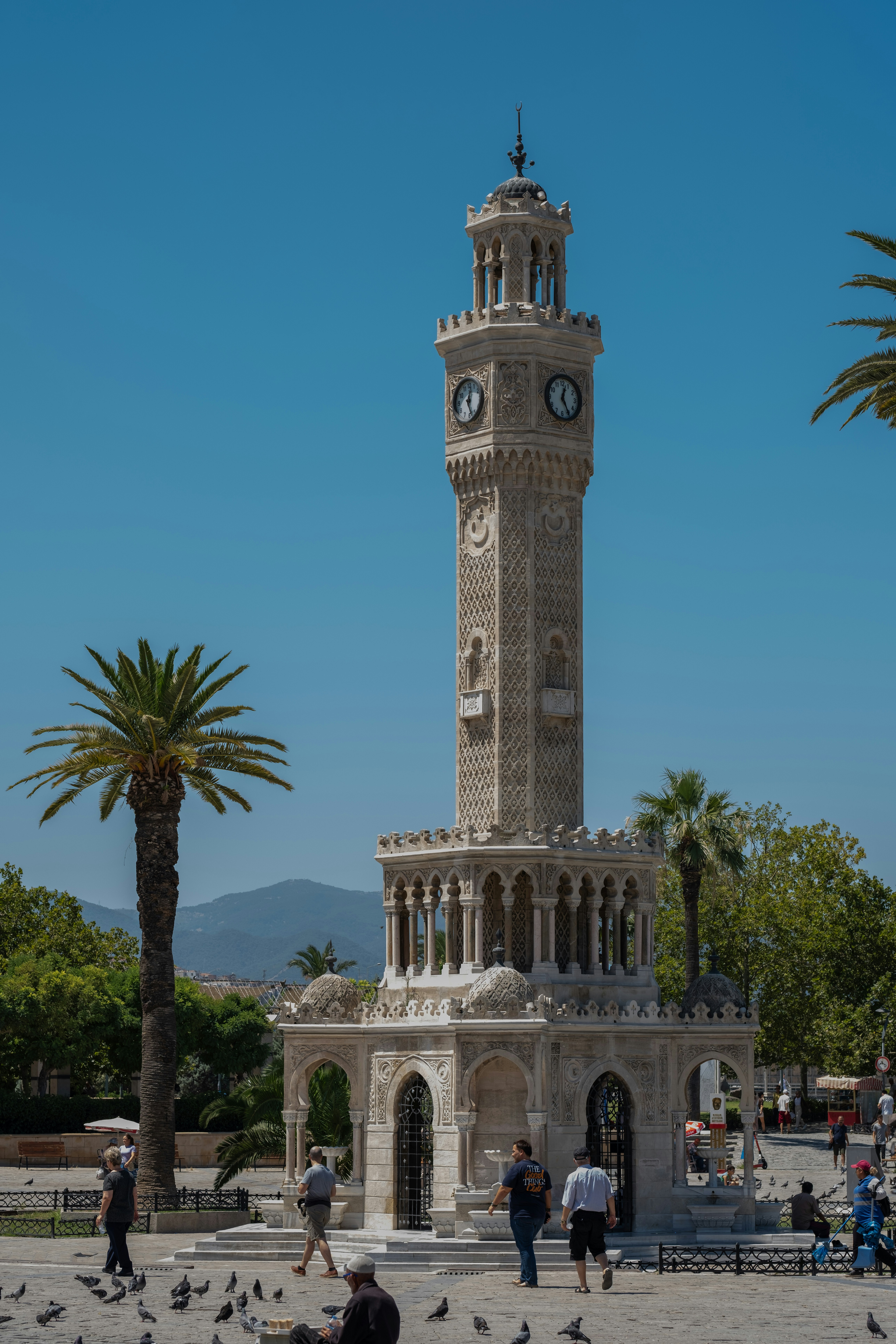 Historic clock tower surrounded by palm trees and visitors, set against a clear blue sky.