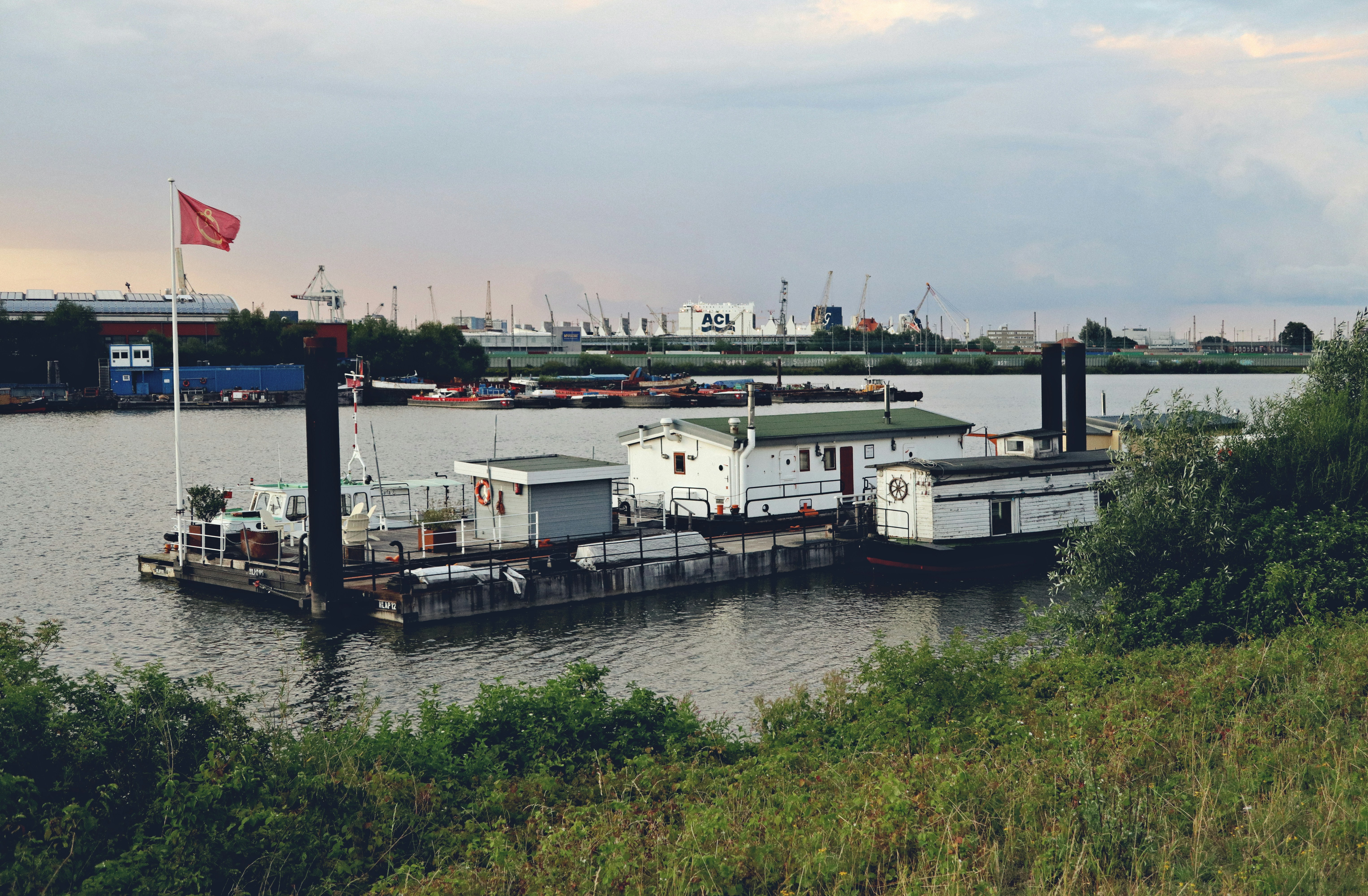 Red Flag Riverside: Moored Houseboats Against a Quiet Harbor Horizon