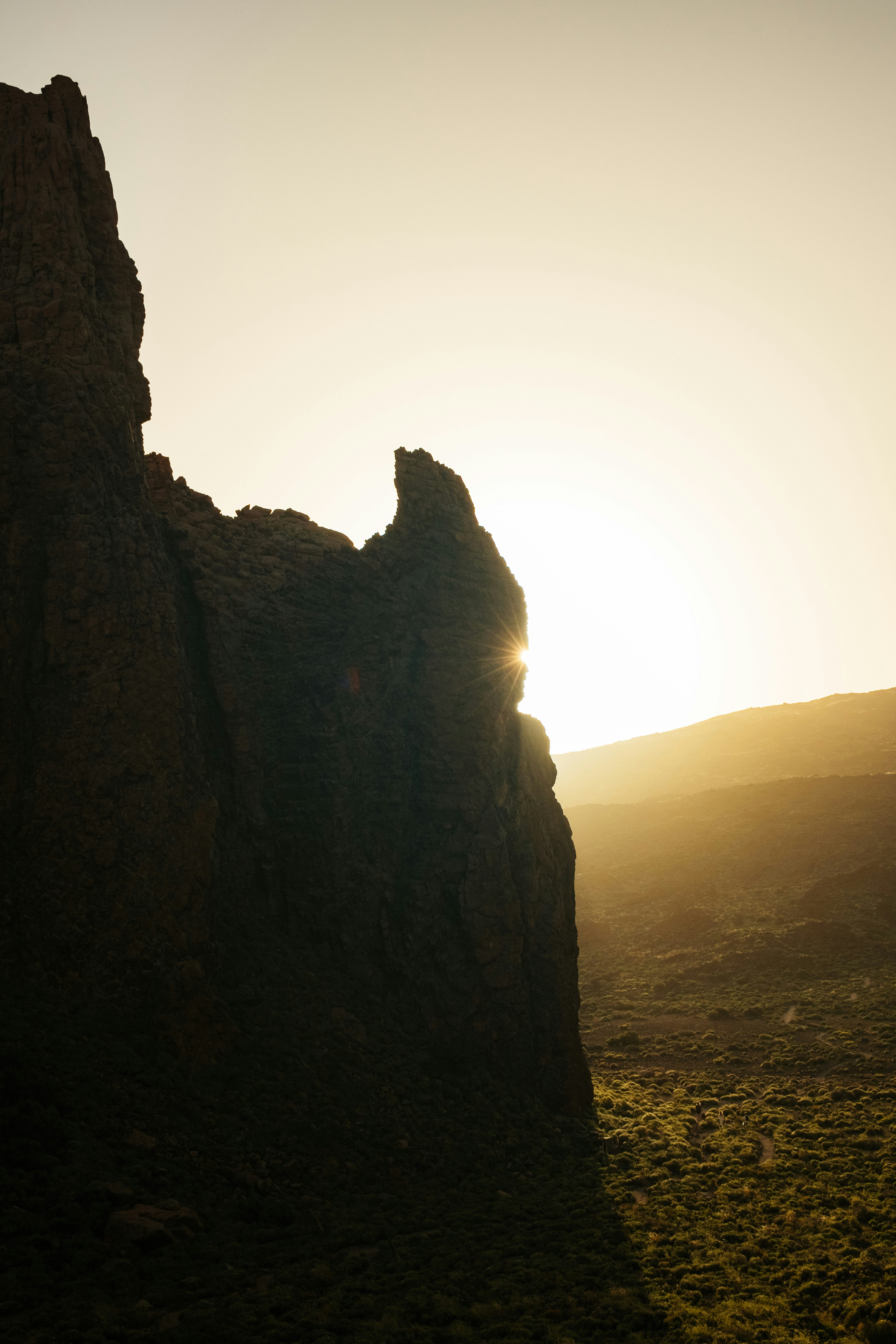 Silhouette of rocky cliffs with the sun peeking over the horizon in a serene landscape.