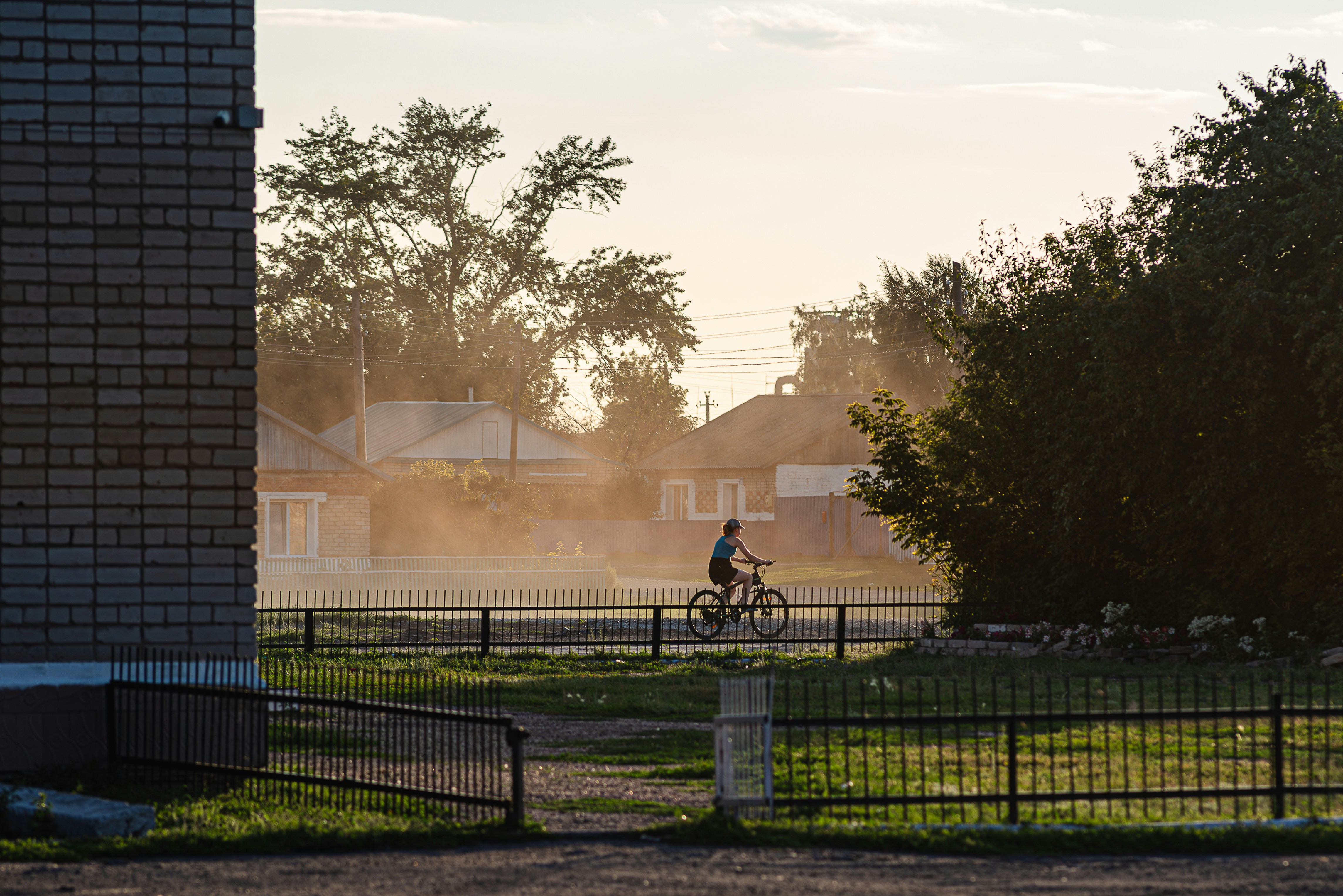 Dust Trails and Quiet Motion: A Cyclist by the Park Fence at Golden Hour
