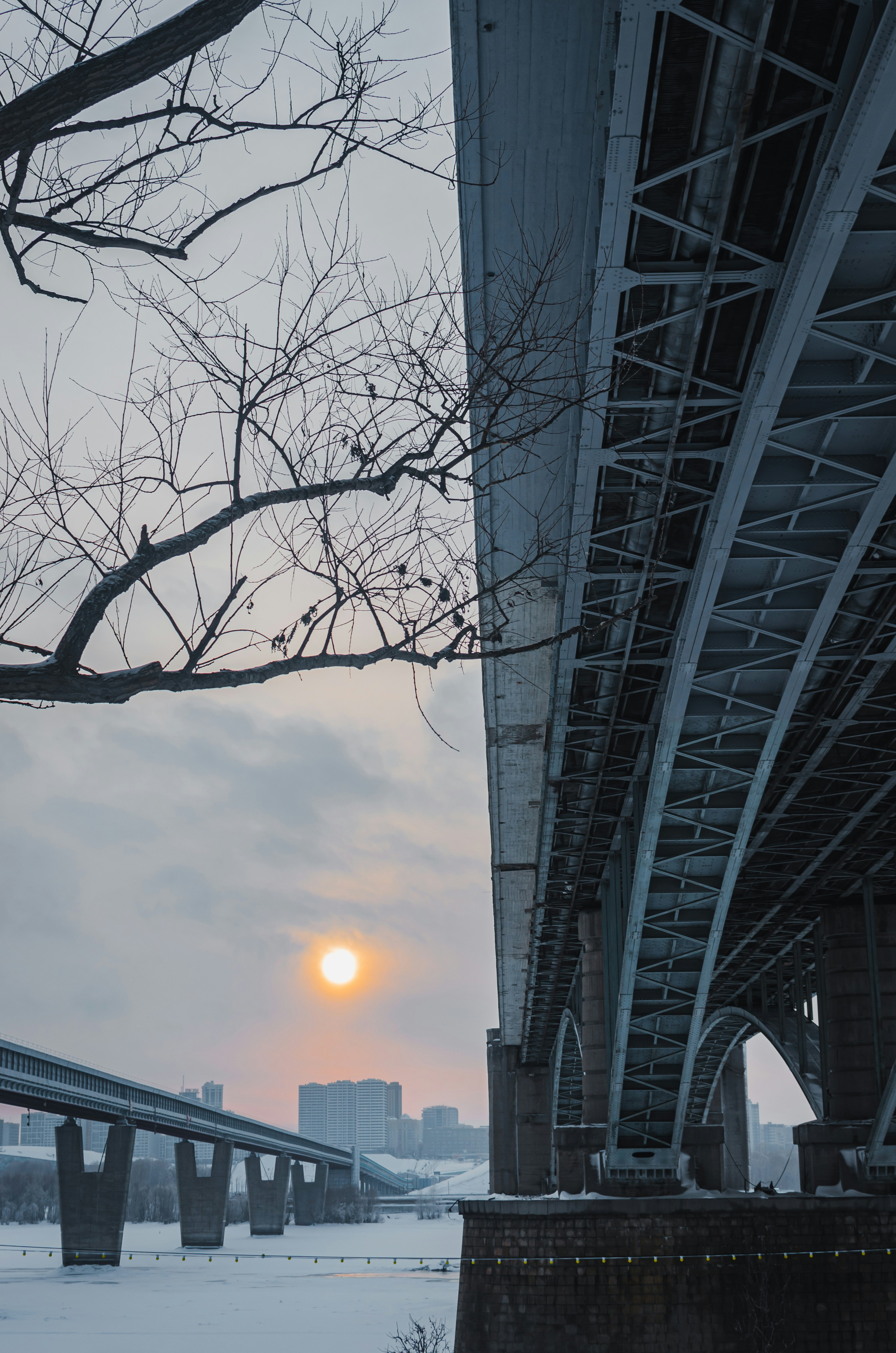 the sun is setting behind a bridge over a frozen river