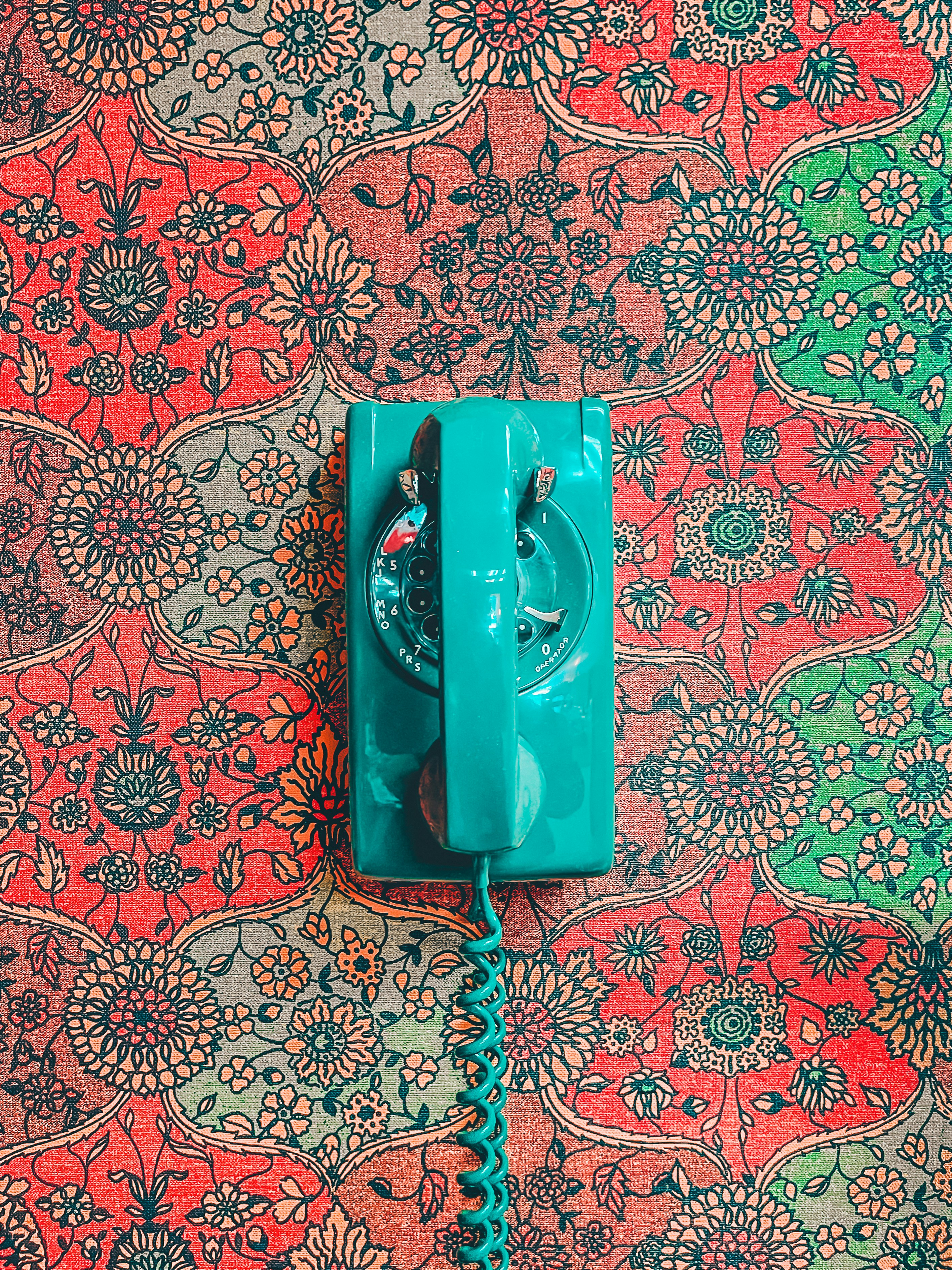 Teal Touch: A Retro Rotary Phone Staples Under a Floral Backdrop
