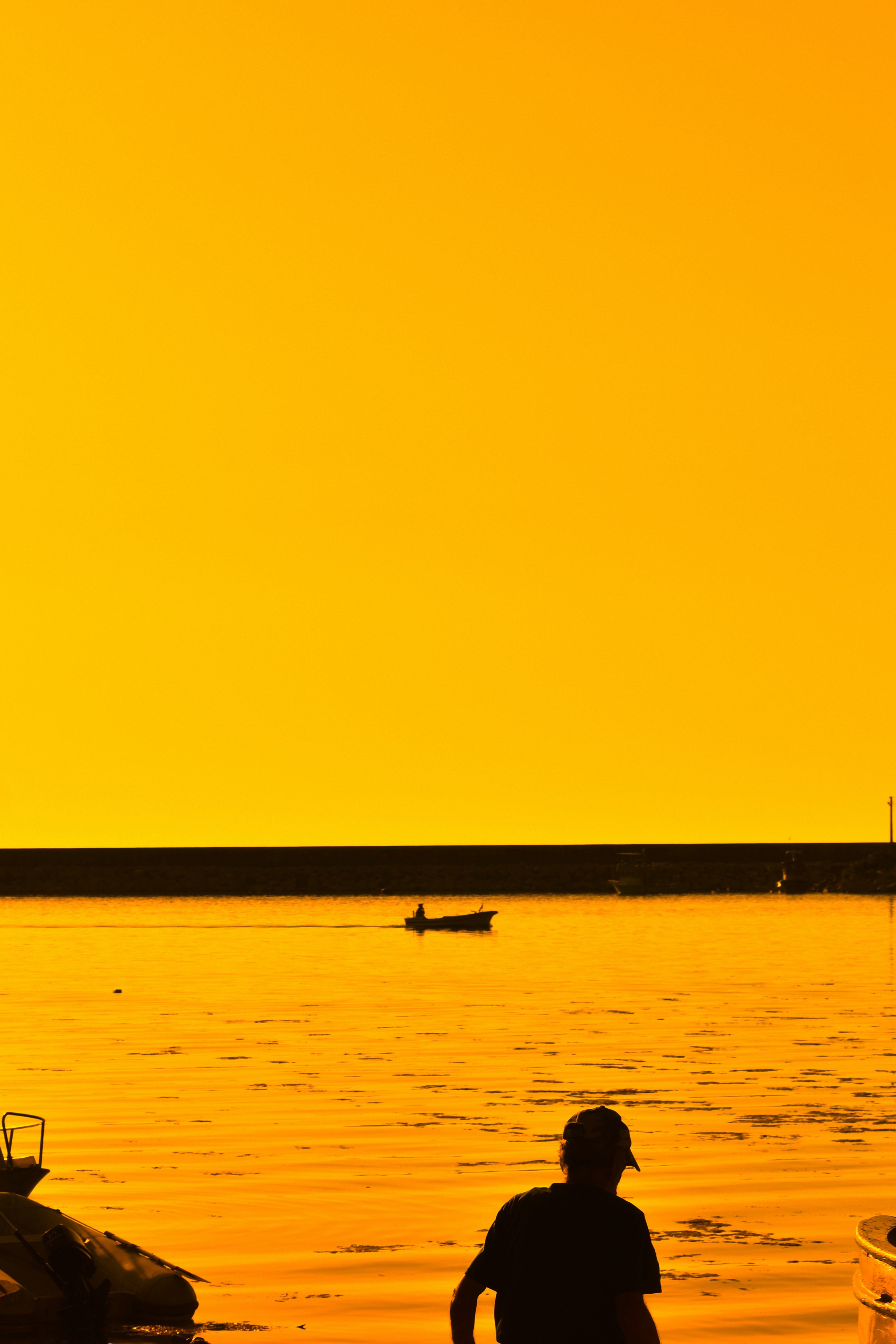 Amber Horizon: A Lone Silhouette and a Small Boat on Quiet Water