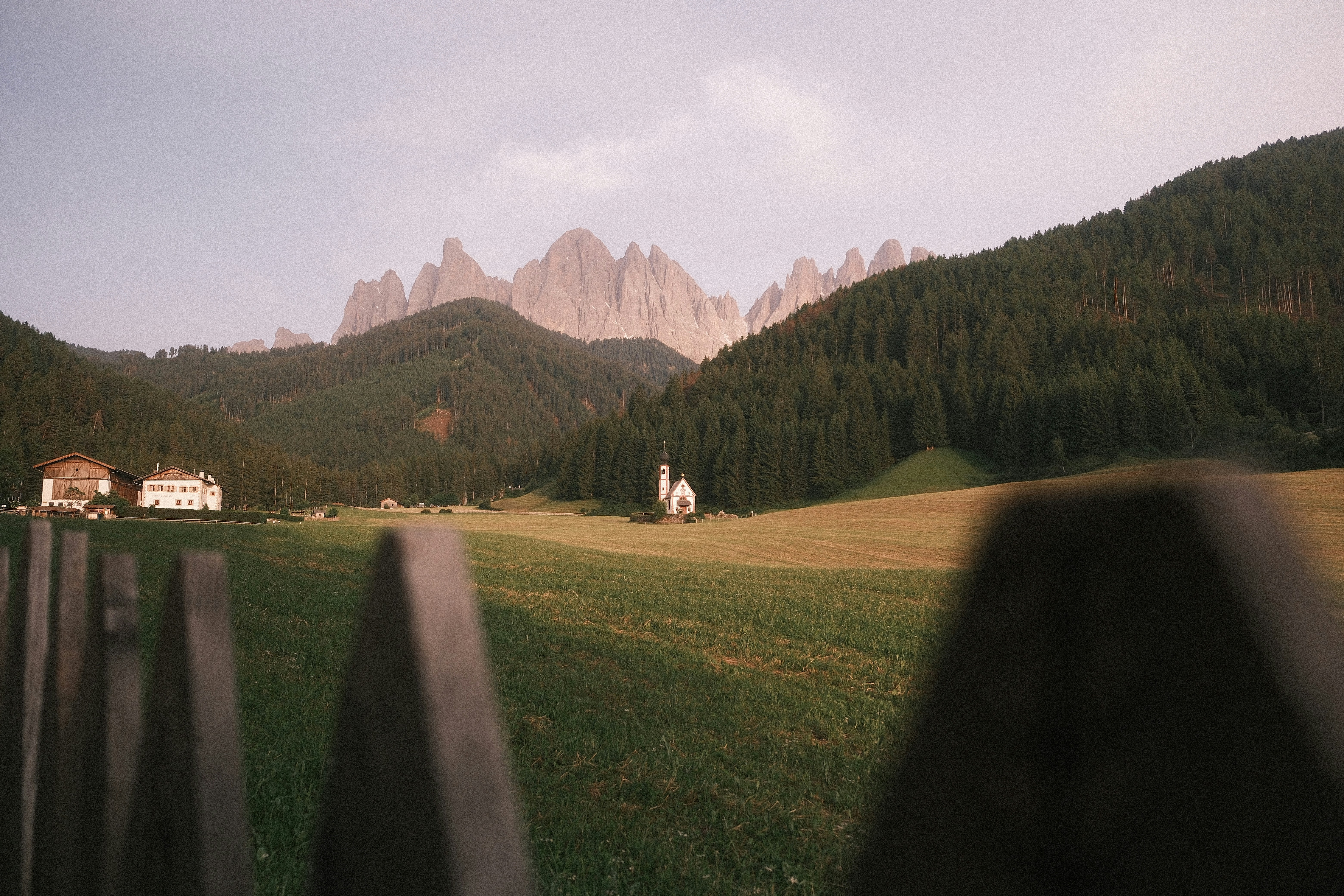 Wooden fence in foreground with a distant mountain range under a pastel sky.