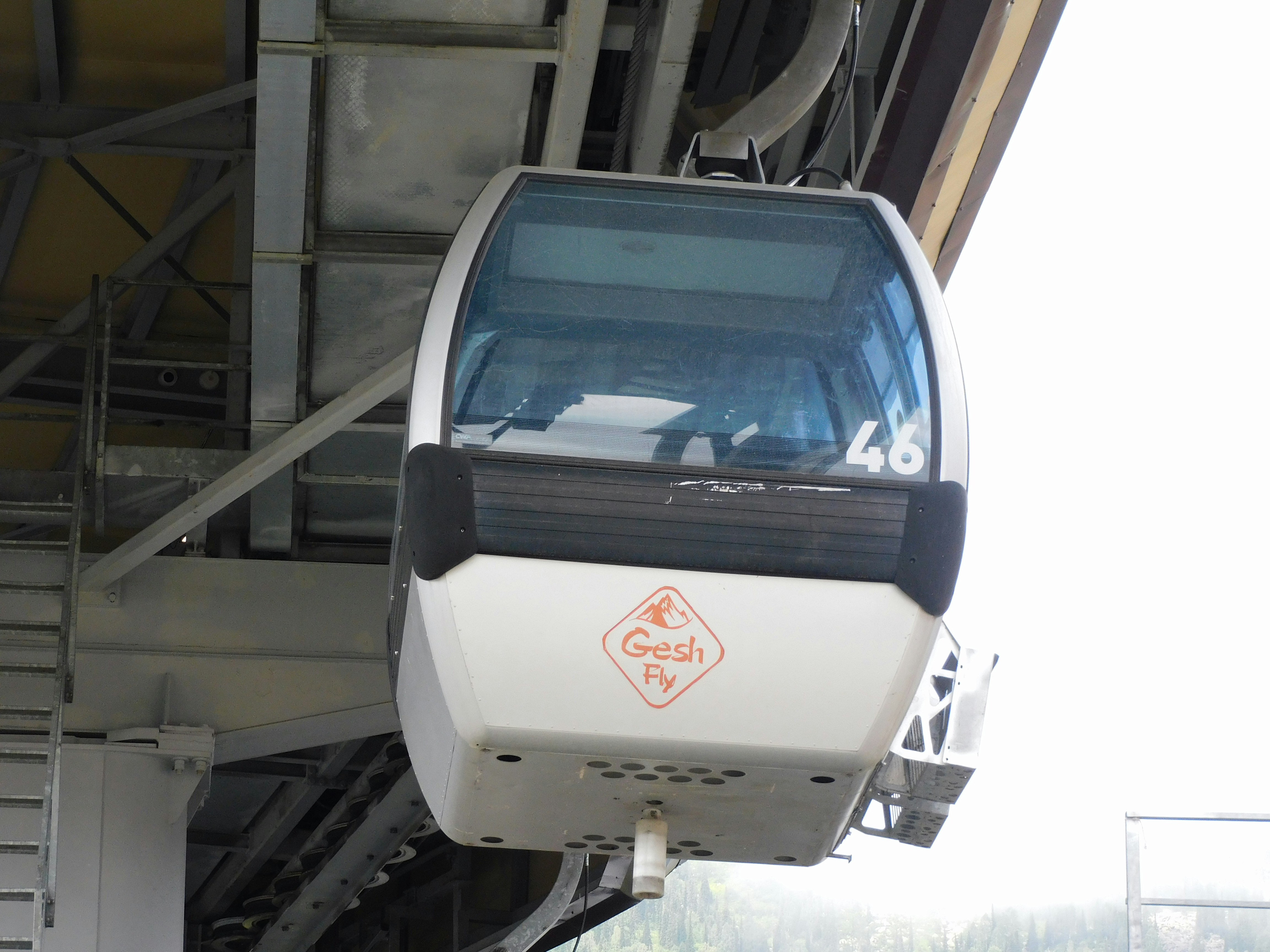 White gondola cabin with the number 46, featuring the orange Gesh Fly logo on its front, suspended above the platform.